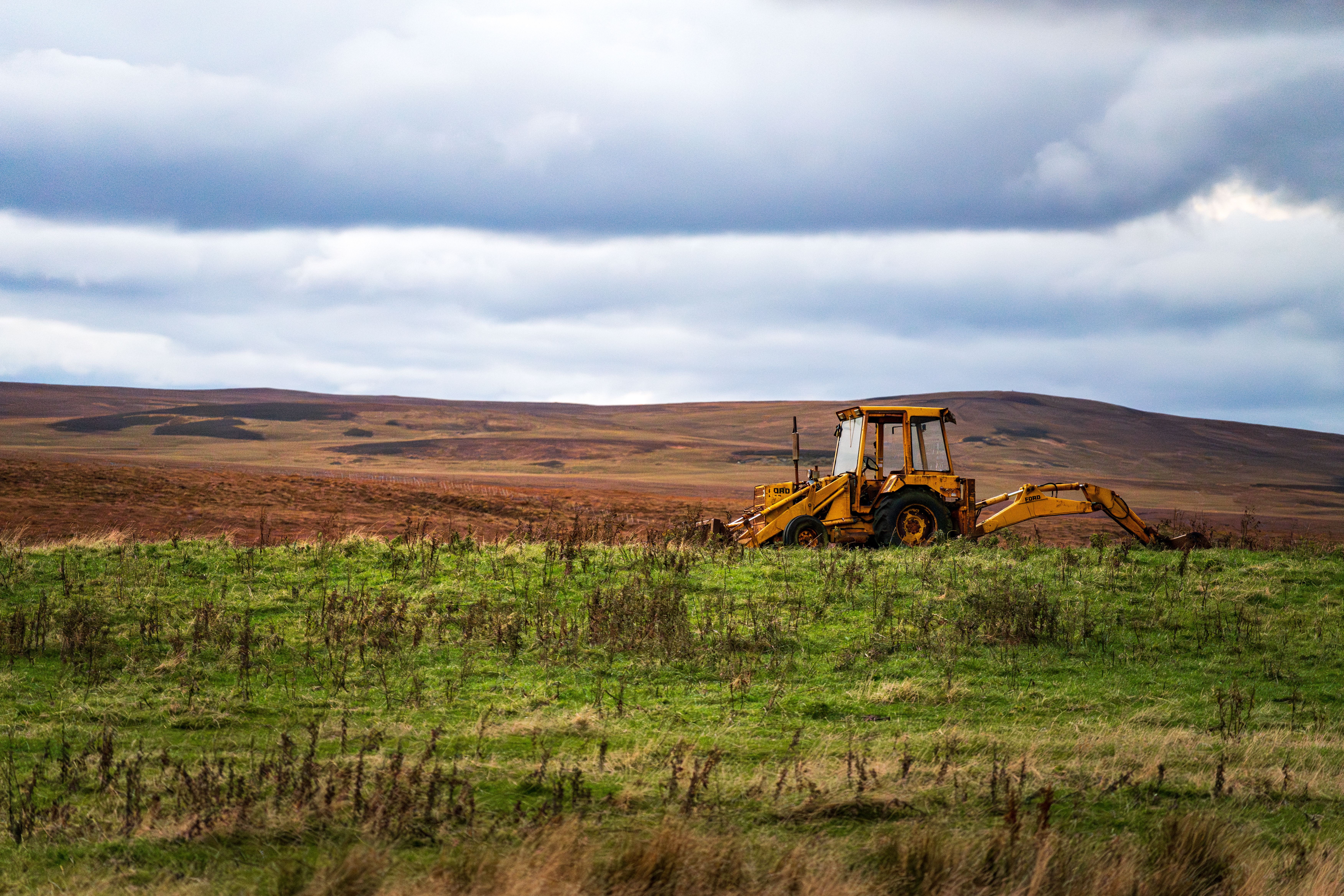 Yellow Backhoe on Vast Green Field Under Cloudy Sky · Free Stock Photo