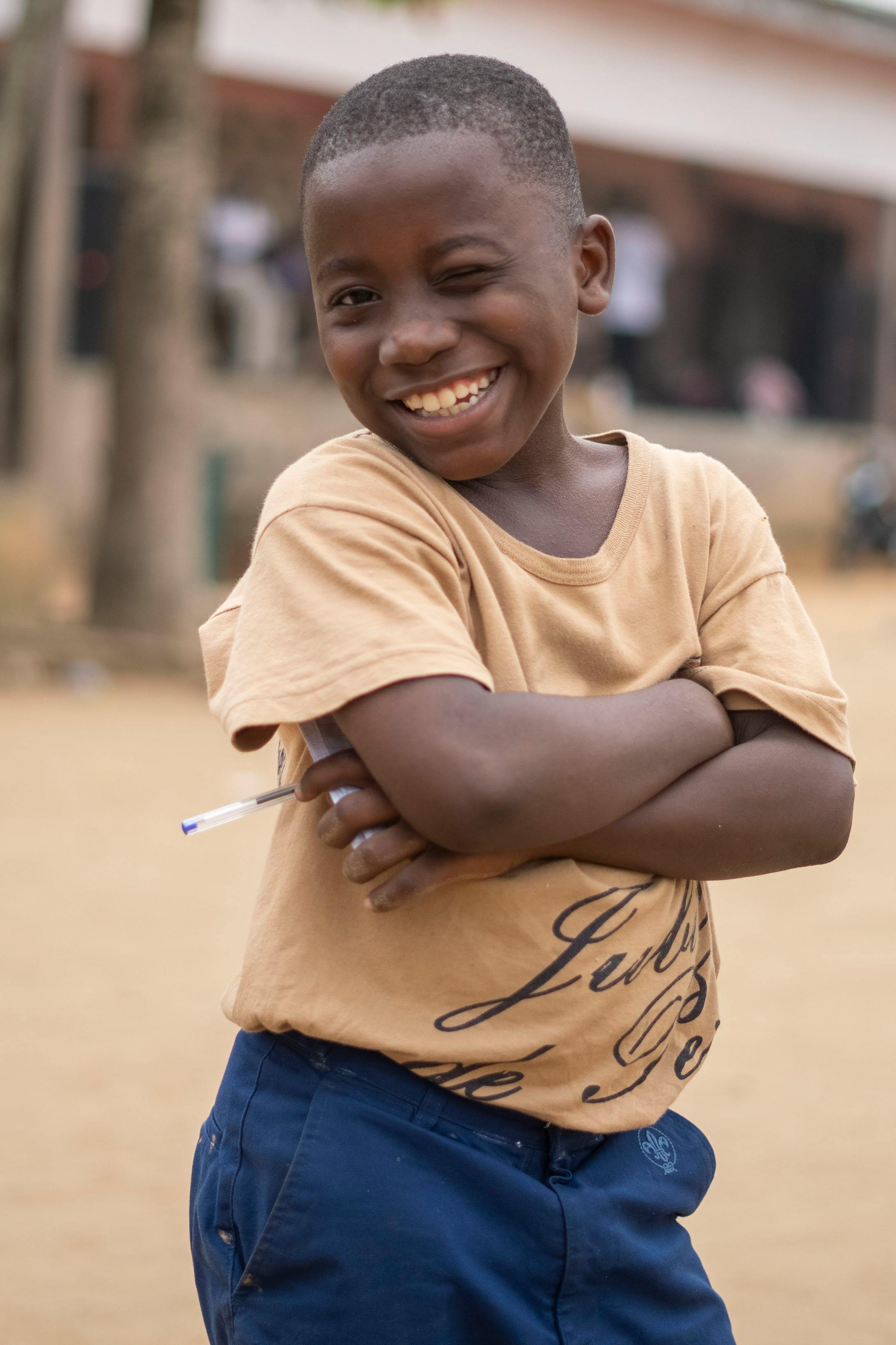 Joyful Child Winking with Arms Crossed Outdoors · Free Stock Photo