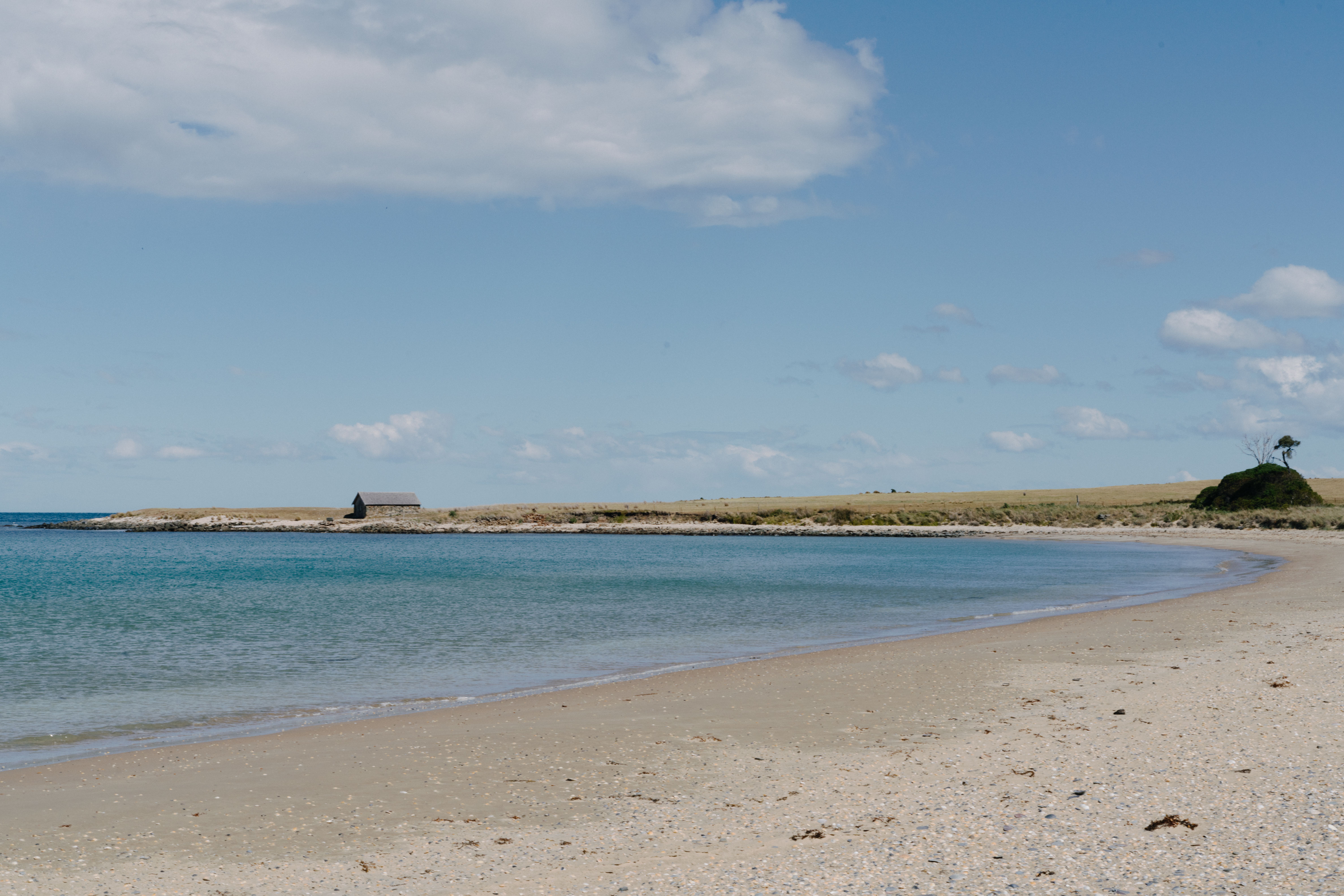 Tranquil Beach with Remote Cabin Under Blue Sky · Free Stock Photo
