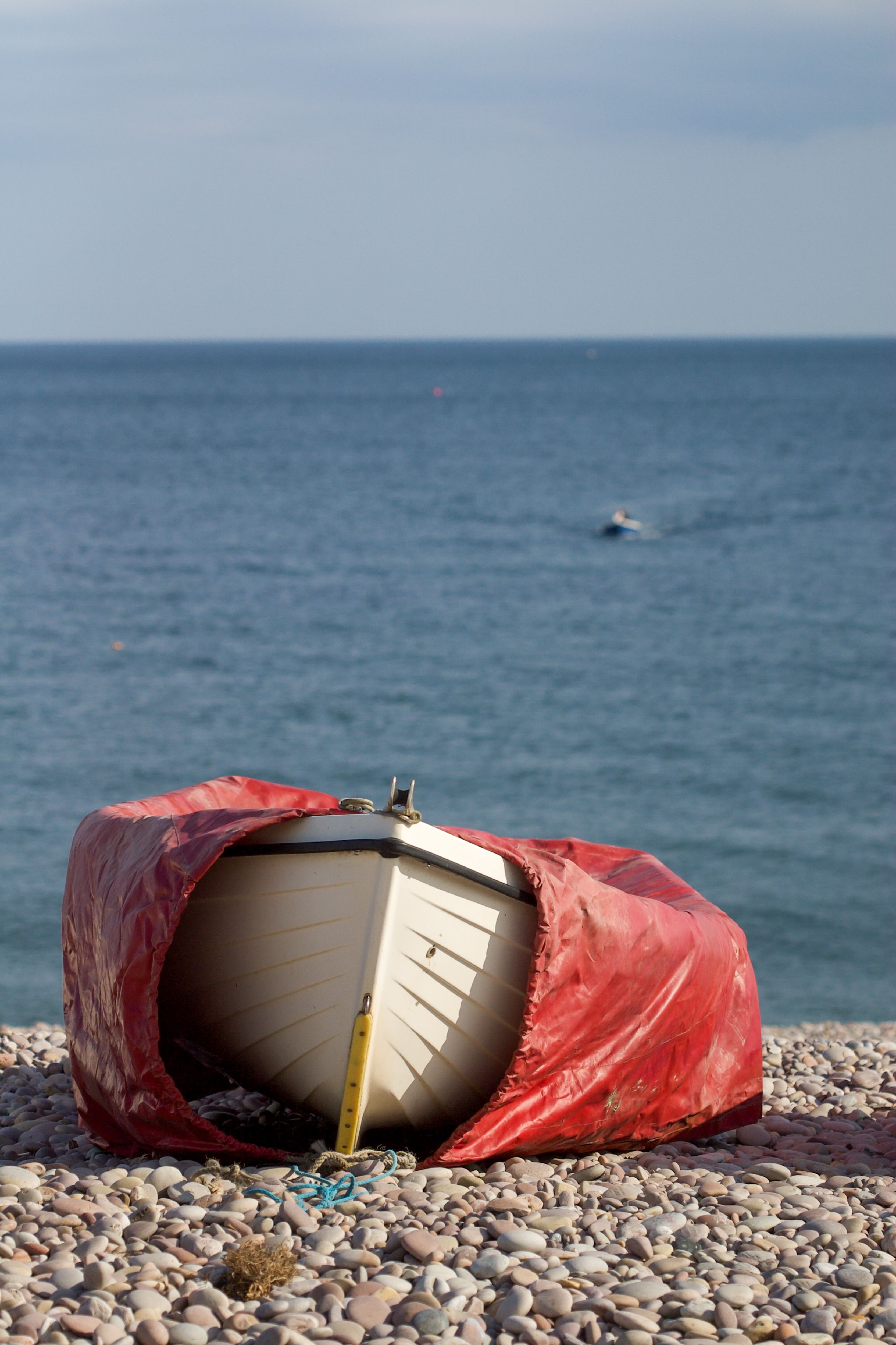 Small Boat Covered with Red Tarp on Pebble Beach · Free Stock Photo