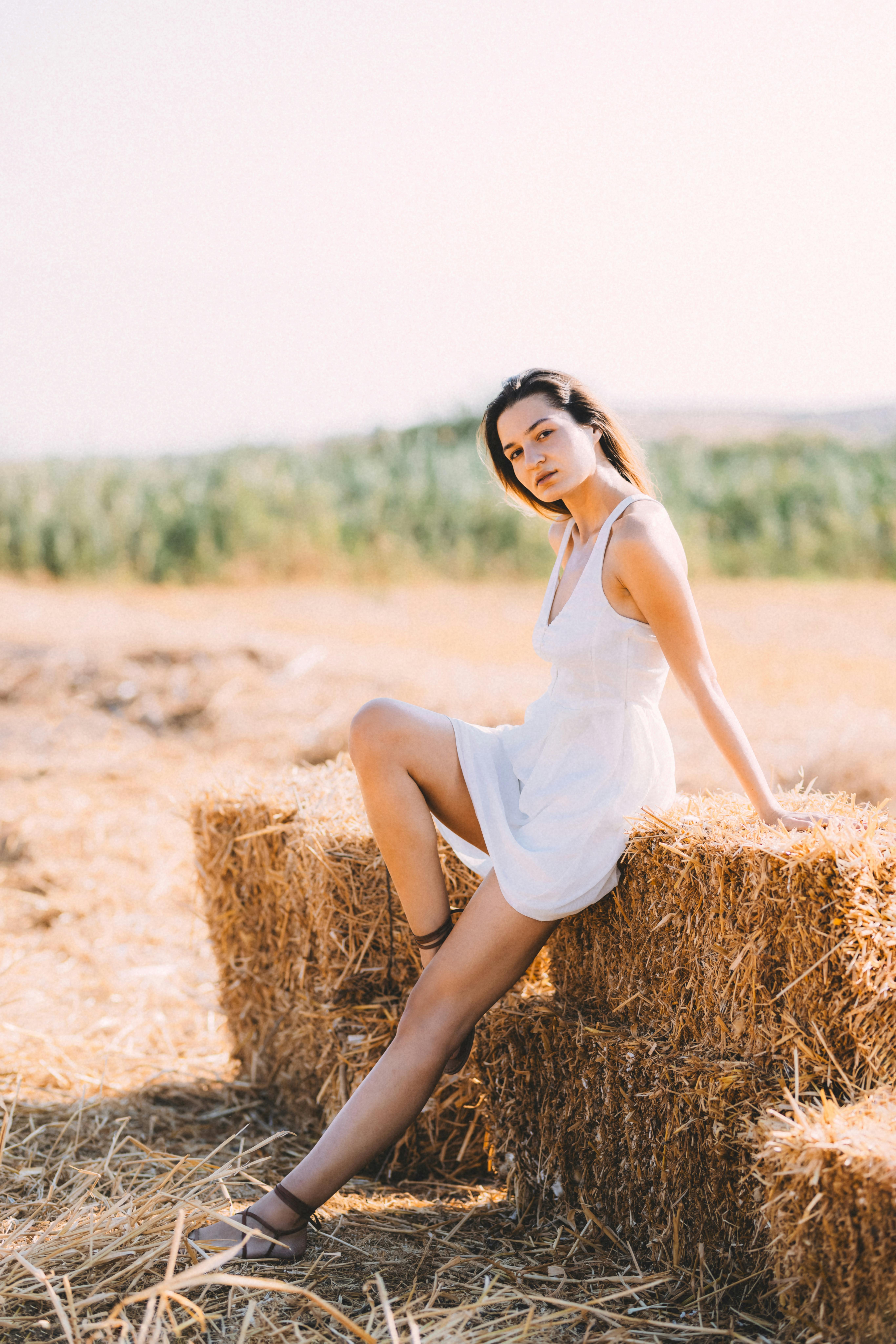 Woman in White Dress Sitting on Hay Bale in Field · Free Stock Photo