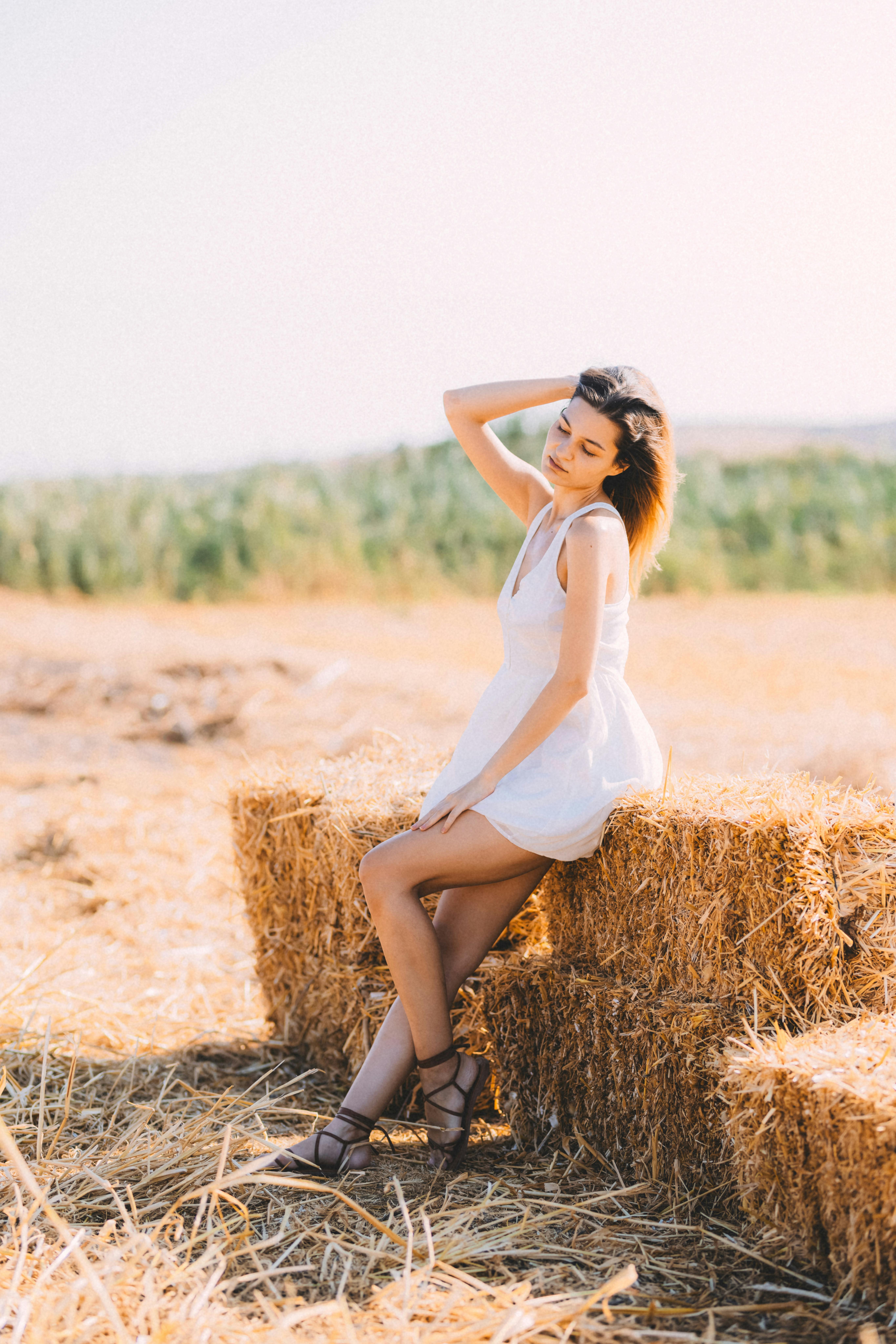 Woman in White Dress Posing on Hay Bale in Field · Free Stock Photo