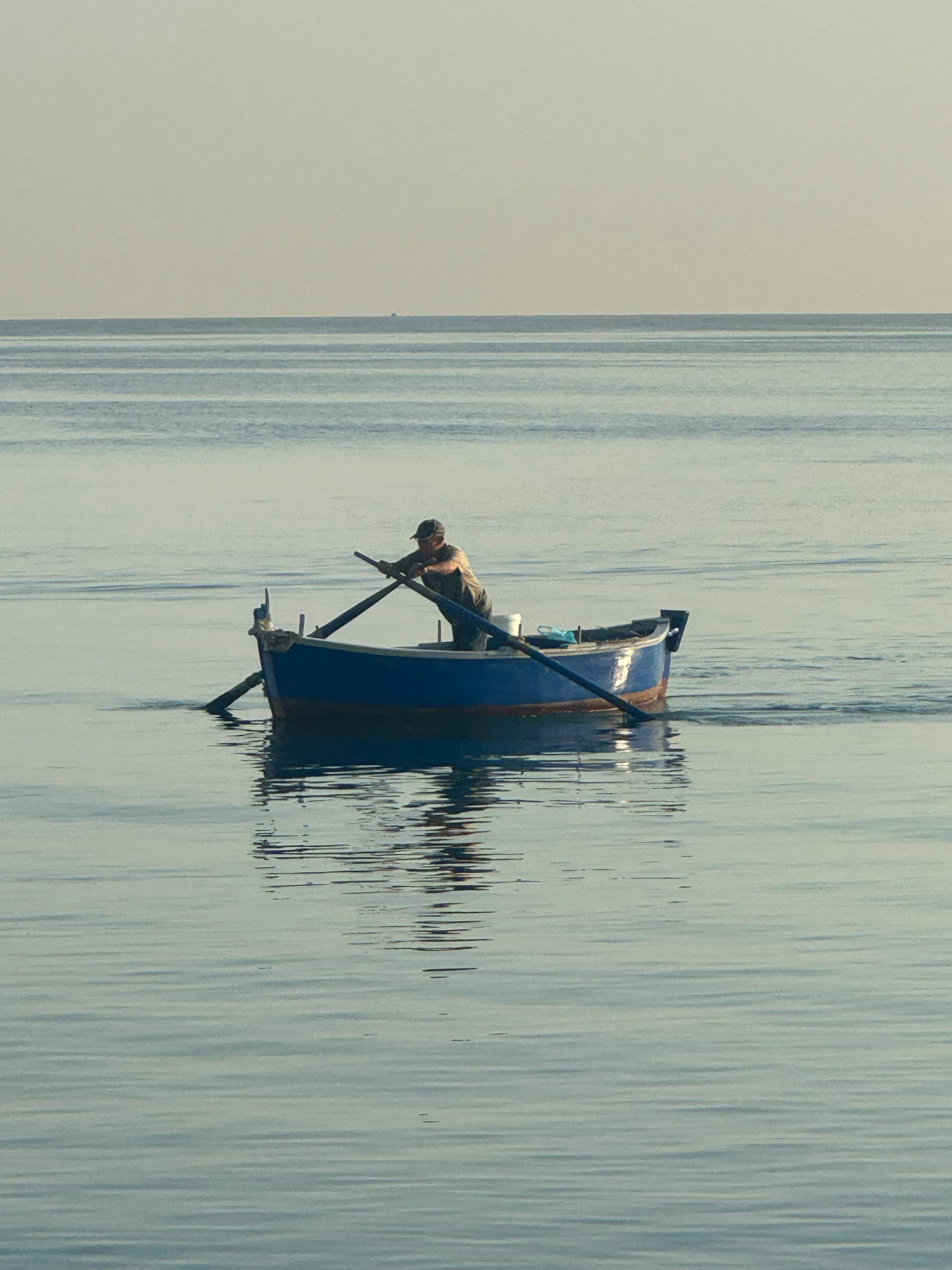 Man rowing blue boat on calm sea · Free Stock Photo
