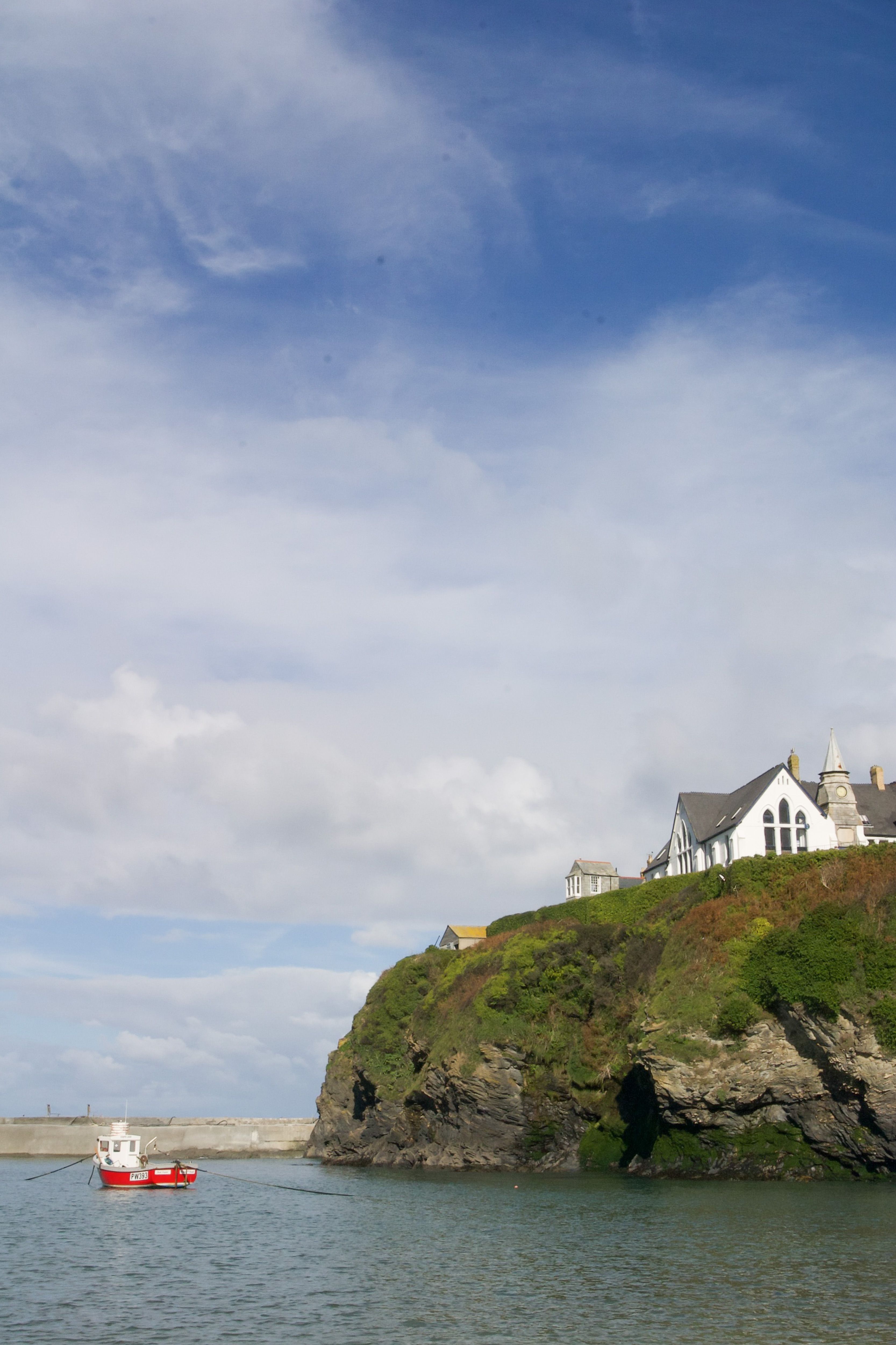 Charming Coastal Cliff and House with Red Boat · Free Stock Photo