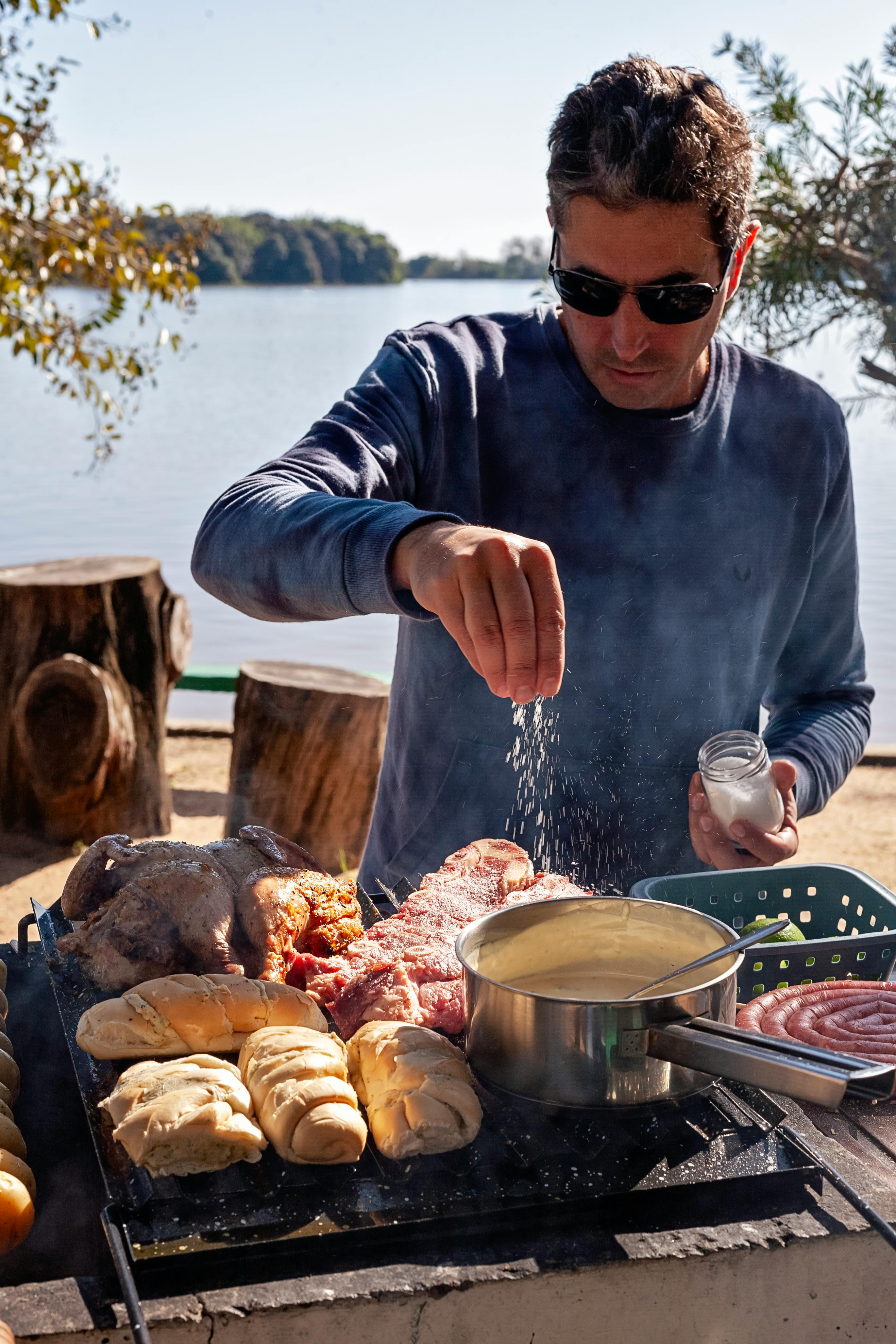 Man Seasoning Outdoor Barbecue by Lake · Free Stock Photo