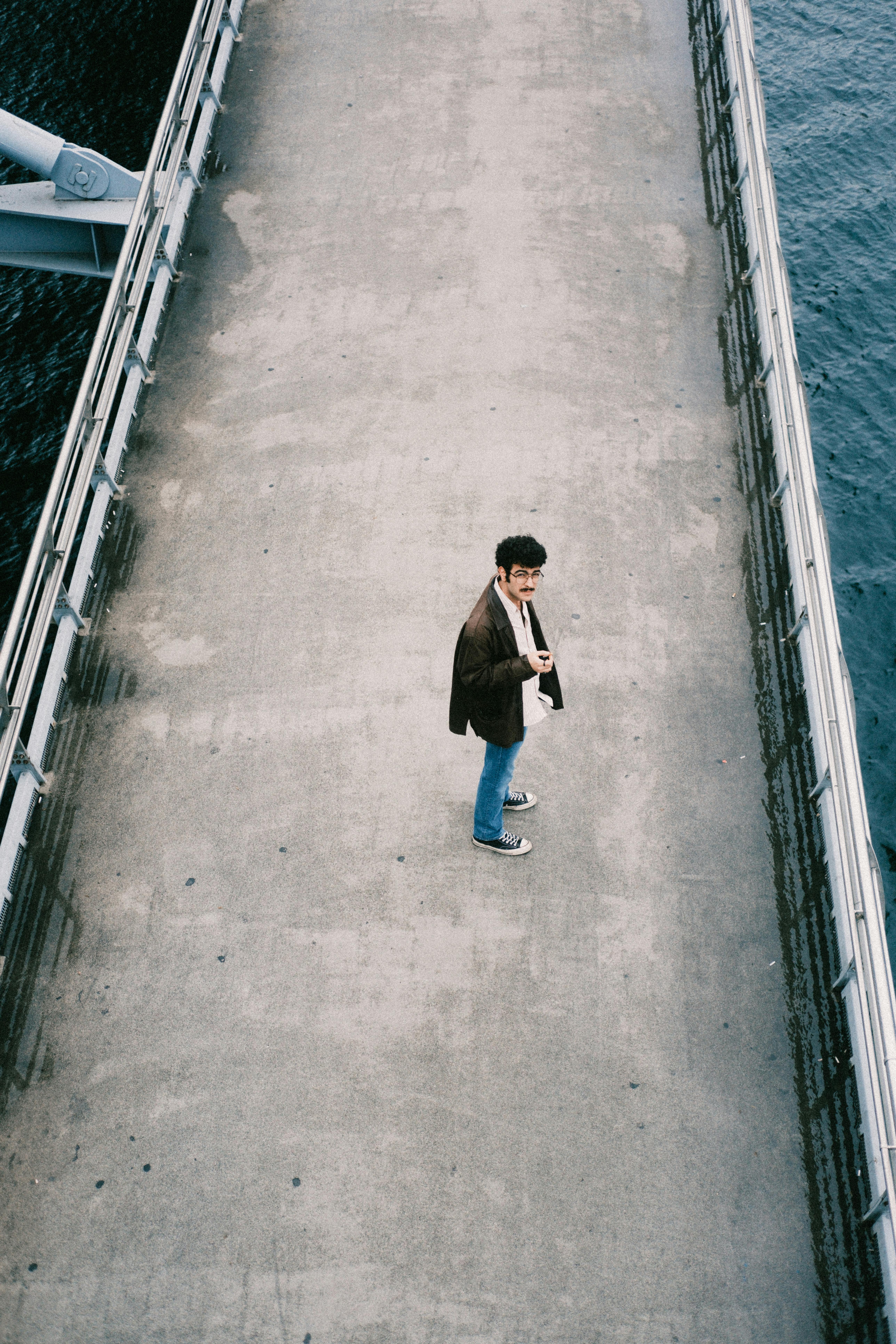 Man Standing on Bridge Overlooking Water · Free Stock Photo