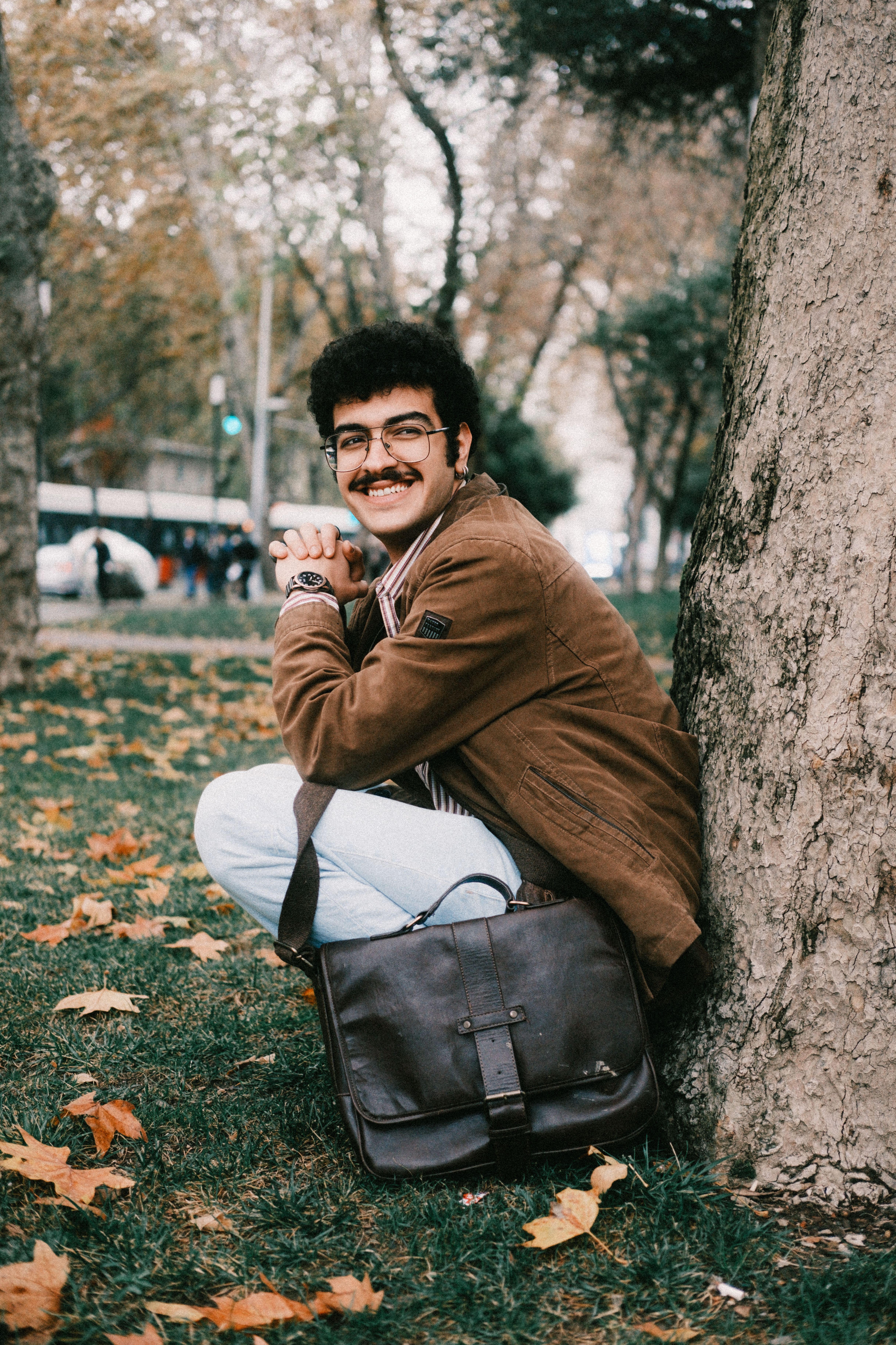 Young man with mustache sitting by tree in autumn park · Free Stock Photo