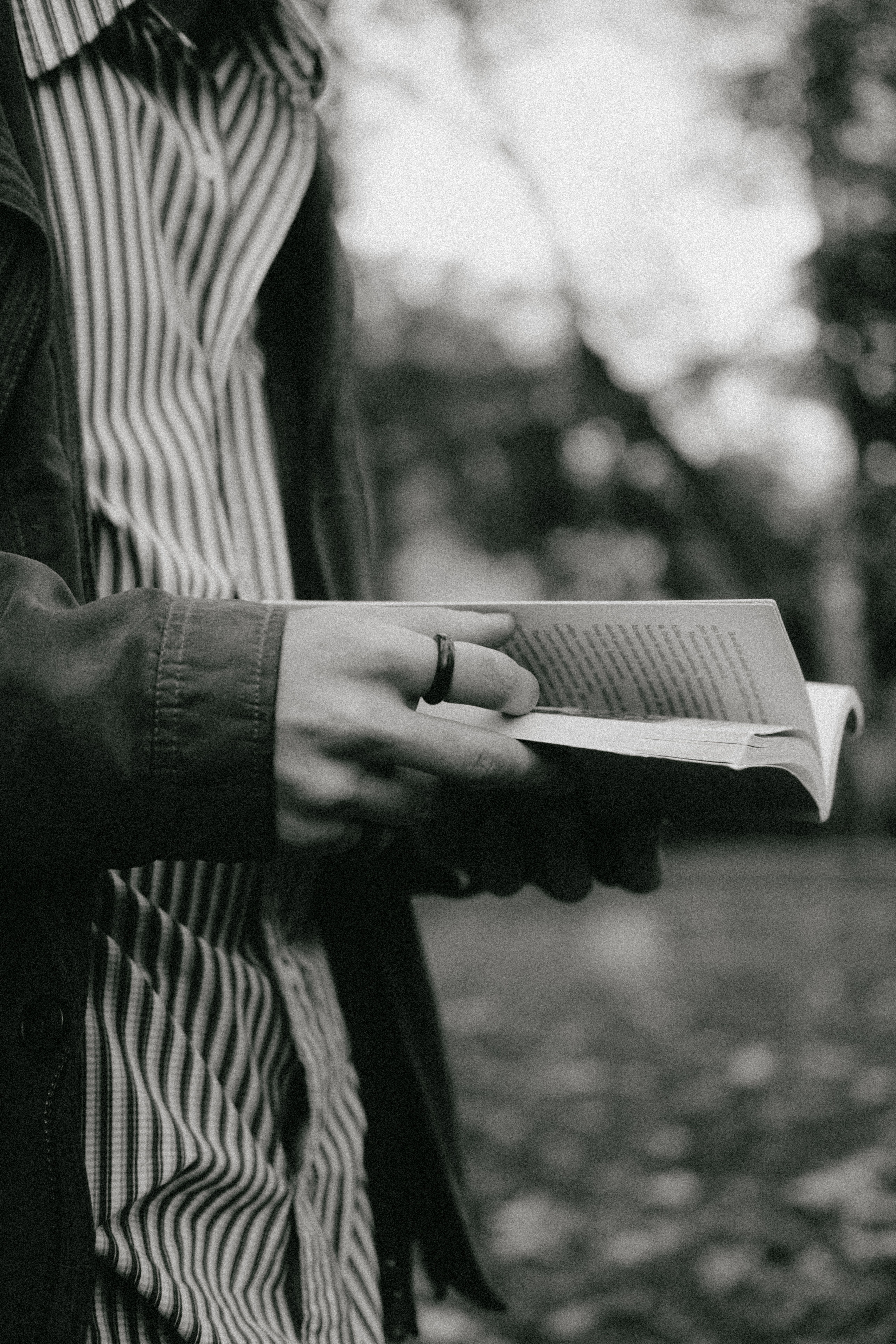 Monochrome Close-Up of Person Reading Book Outdoors · Free Stock Photo