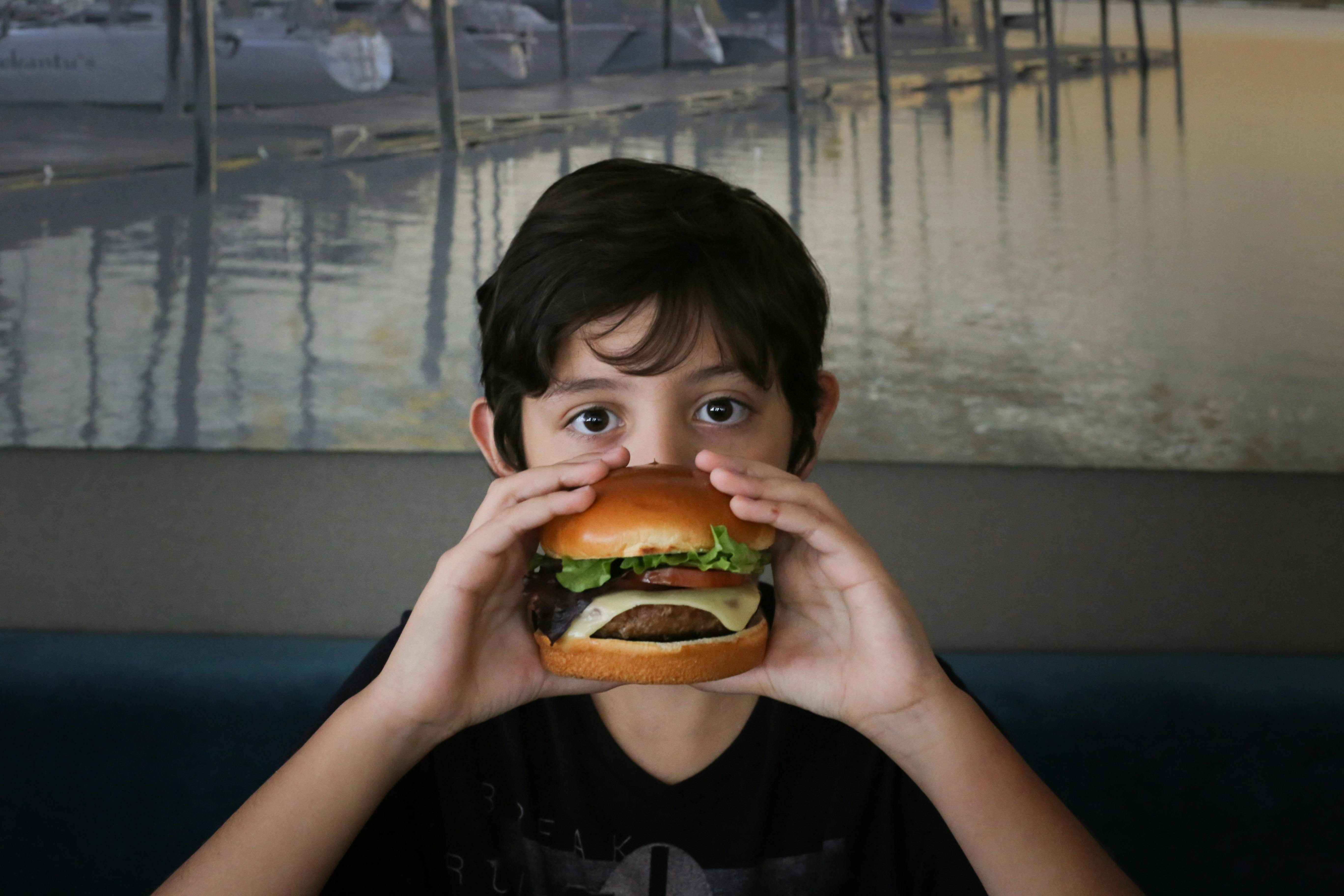 Child Enjoying a Delicious Cheeseburger Indoors · Free Stock Photo