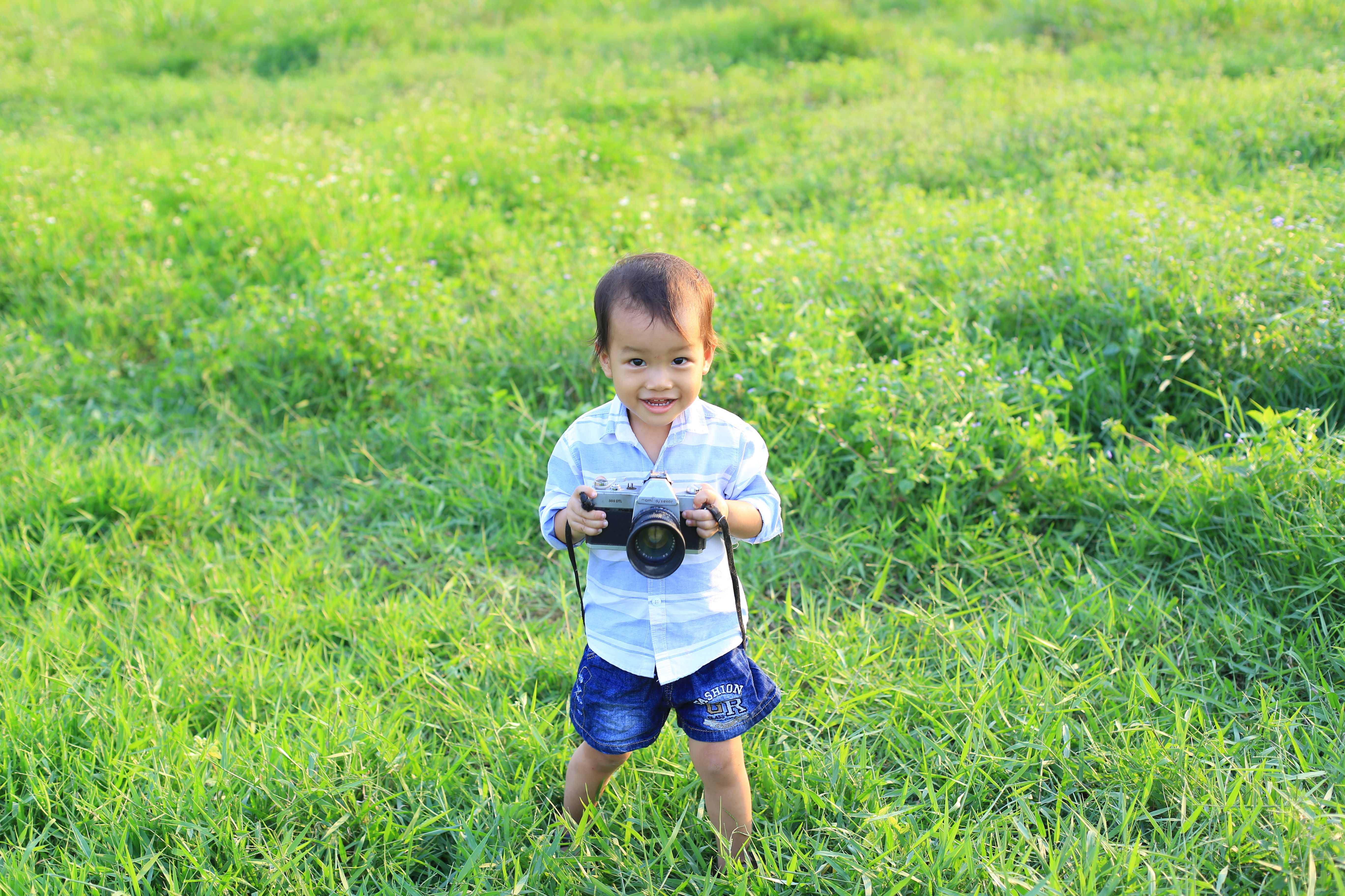 Boy Using Camera Near Green Leaf Plants · Free Stock Photo
