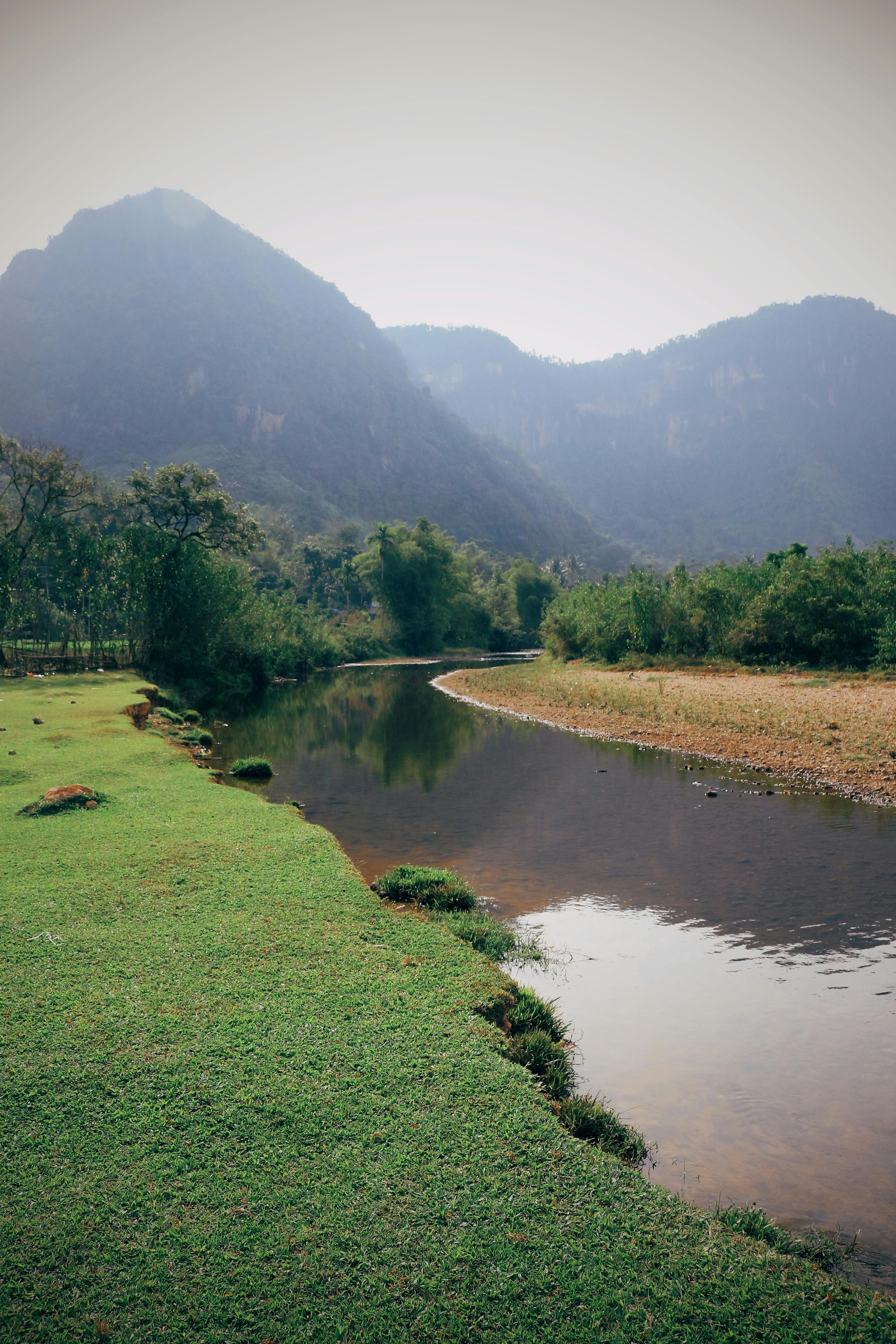 Narrow river between lawns near mountains in countryside · Free Stock Photo