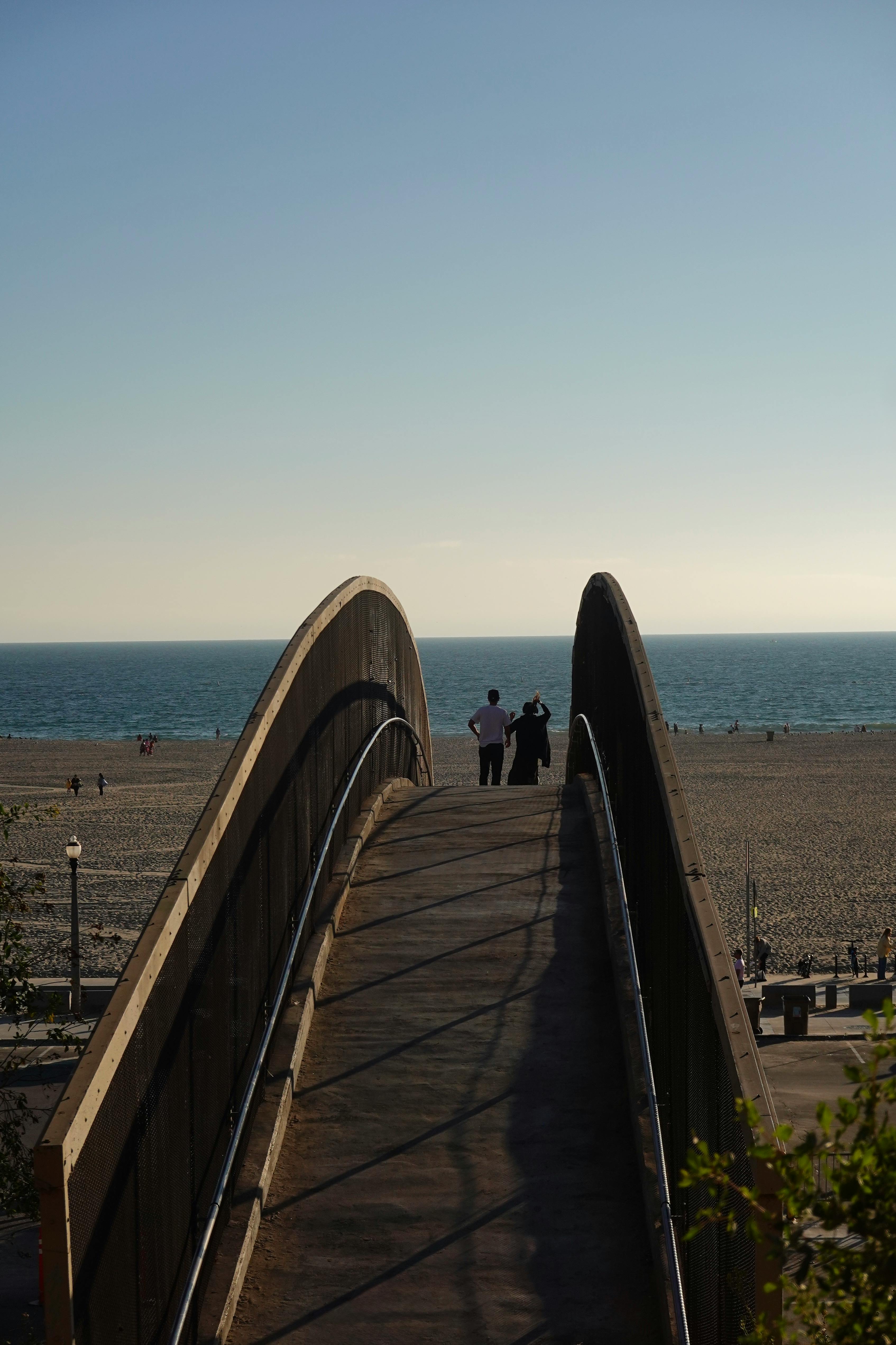 Couple Walking on Seaside Bridge at Sunset · Free Stock Photo