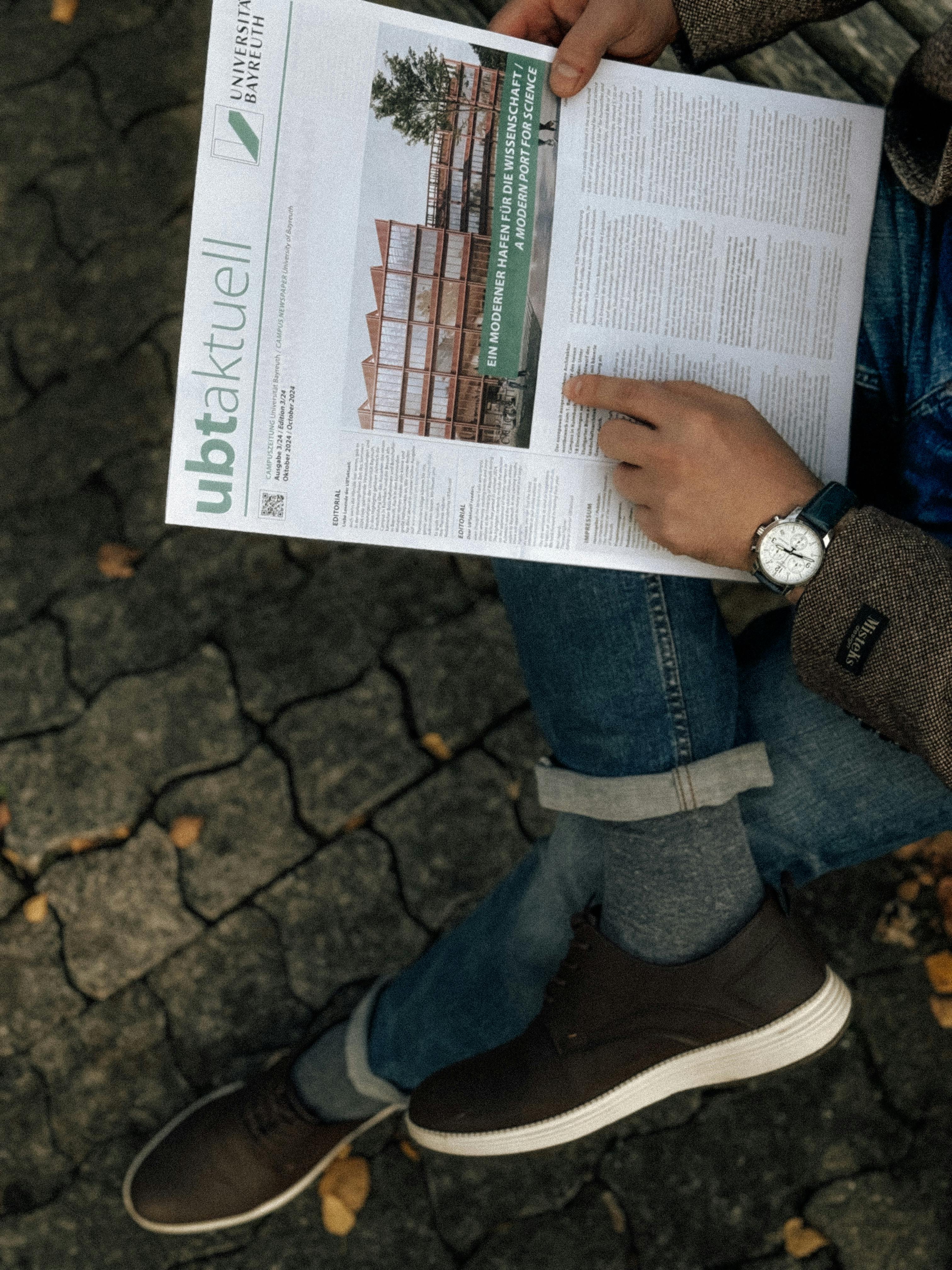 Person Reading UBT Aktuell Newspaper Outdoors · Free Stock Photo