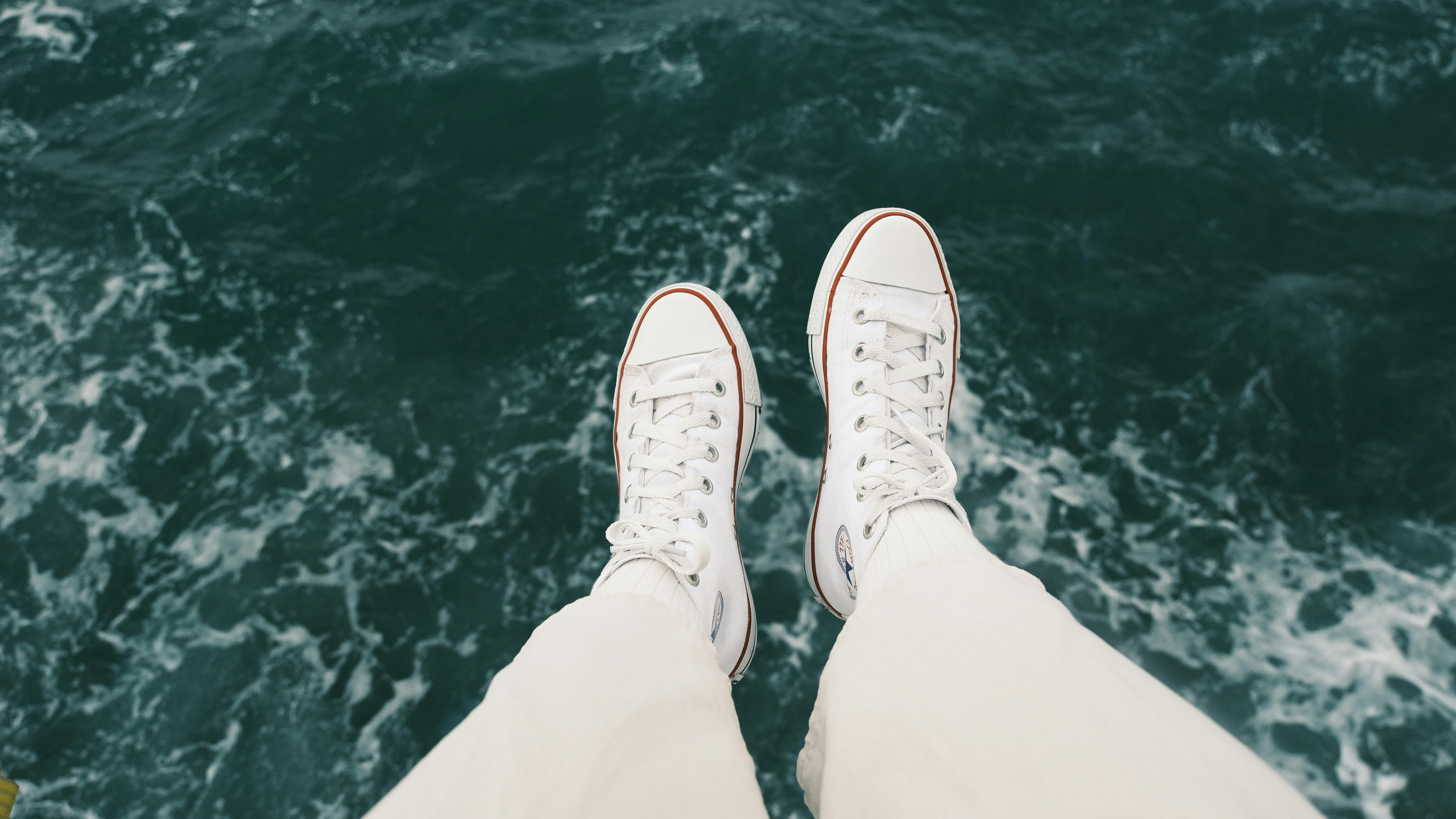 Person dangling feet over ocean wearing white sneakers · Free Stock Photo