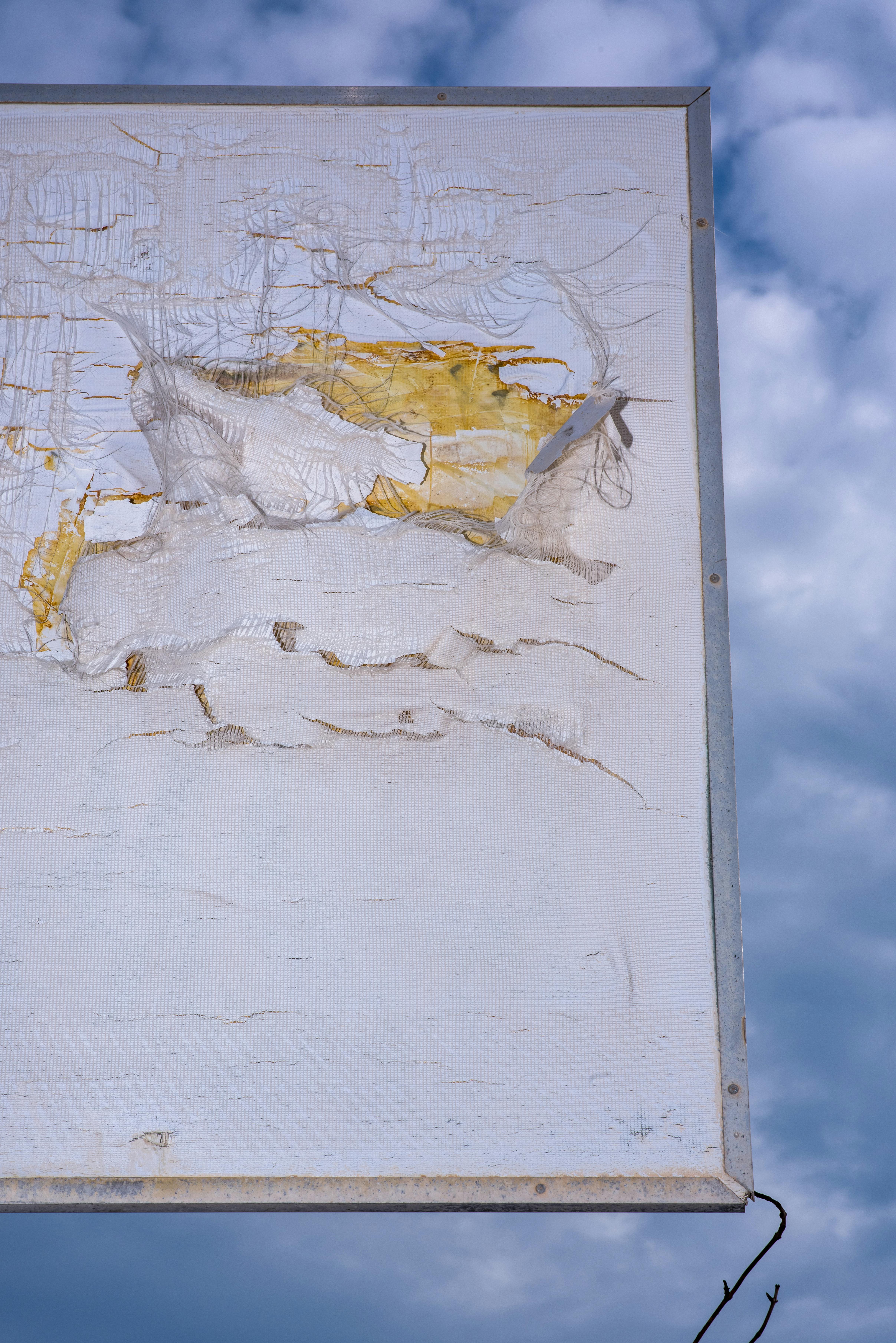 Weathered Billboard with Torn Fabric Under Cloudy Sky · Free Stock Photo