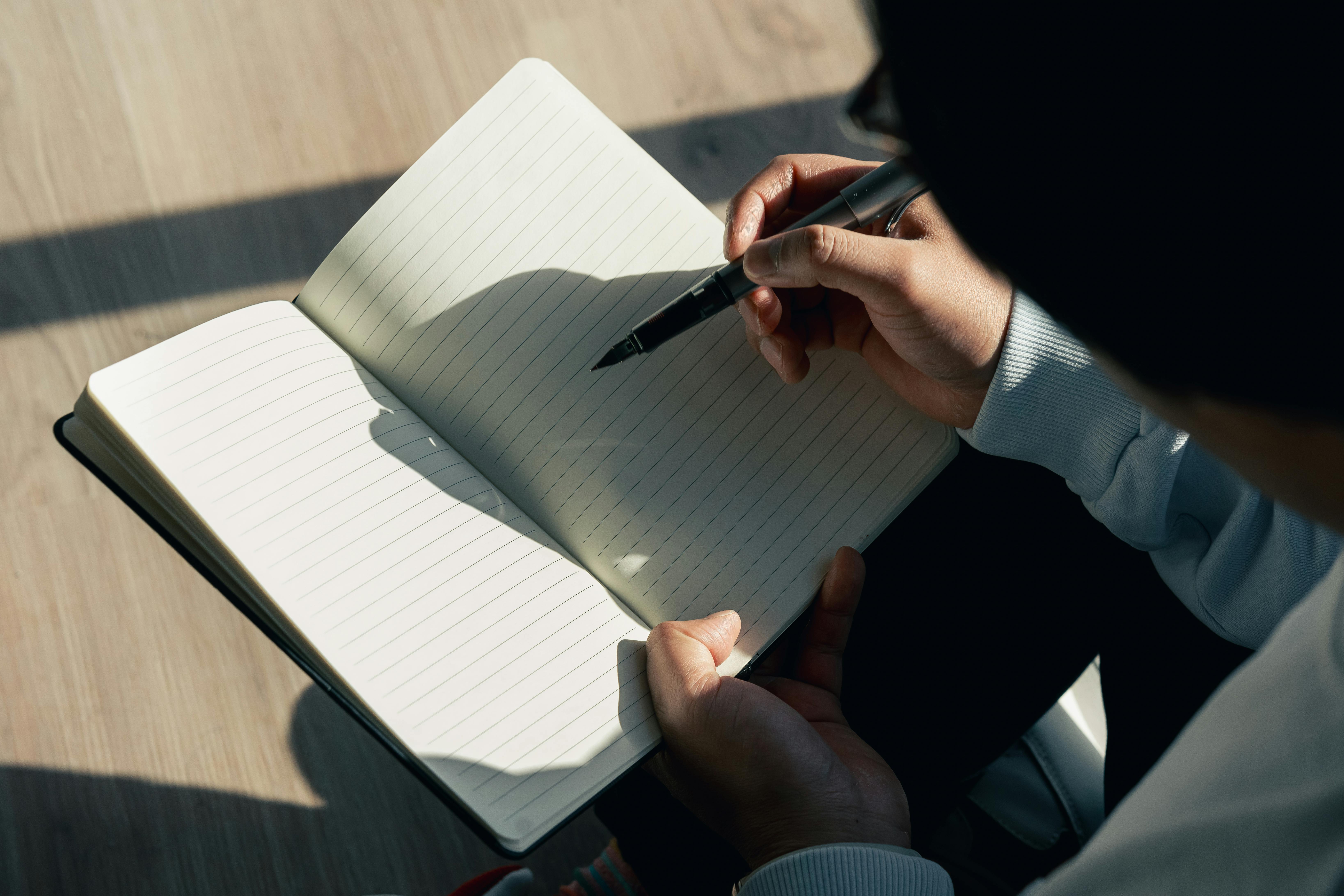 Person Writing in Notebook with Pen in Sunlight · Free Stock Photo