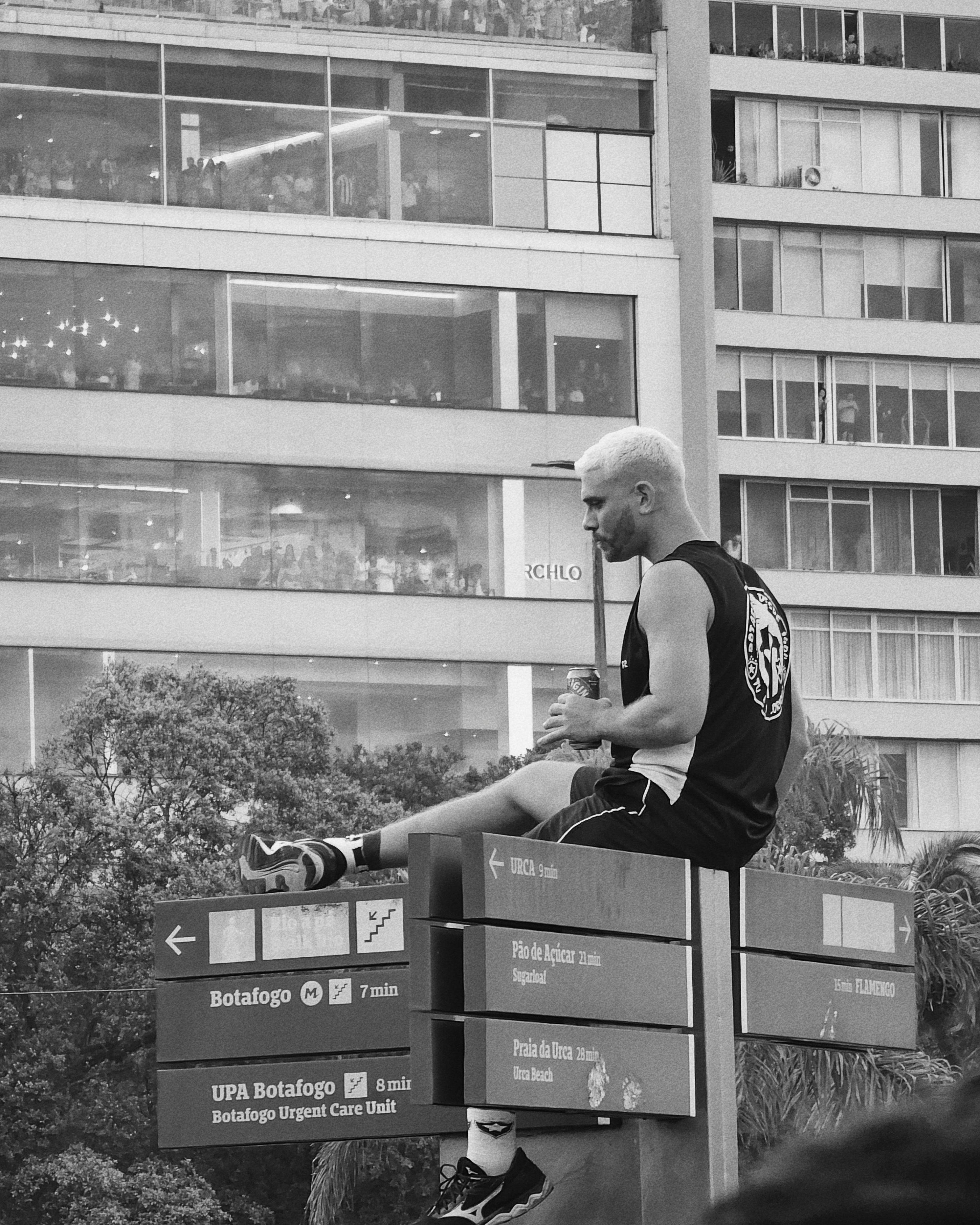 Man Sitting on Sign in Urban Environment · Free Stock Photo
