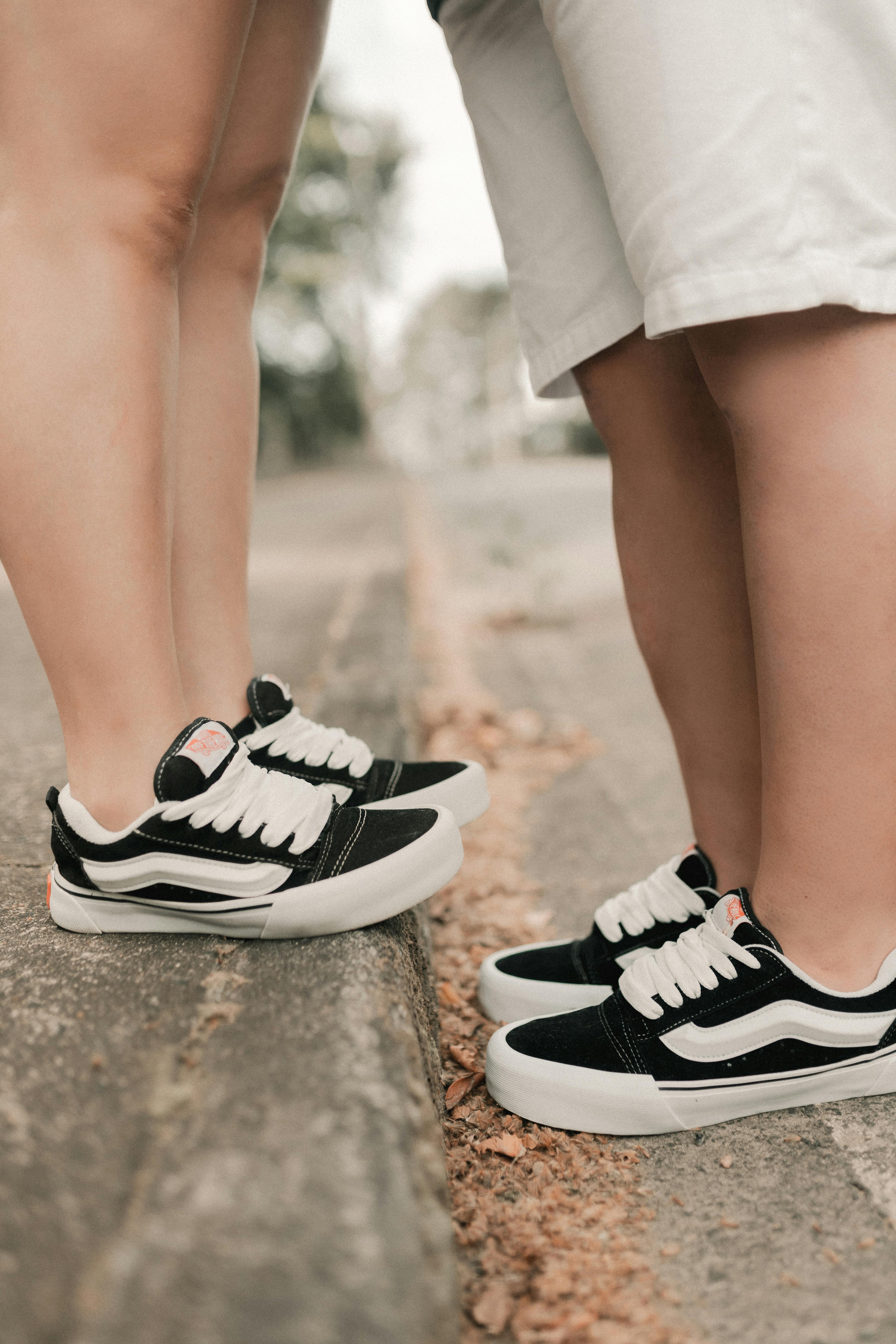 Close-up of Couple's Feet in Sneakers on a Curb · Free Stock Photo