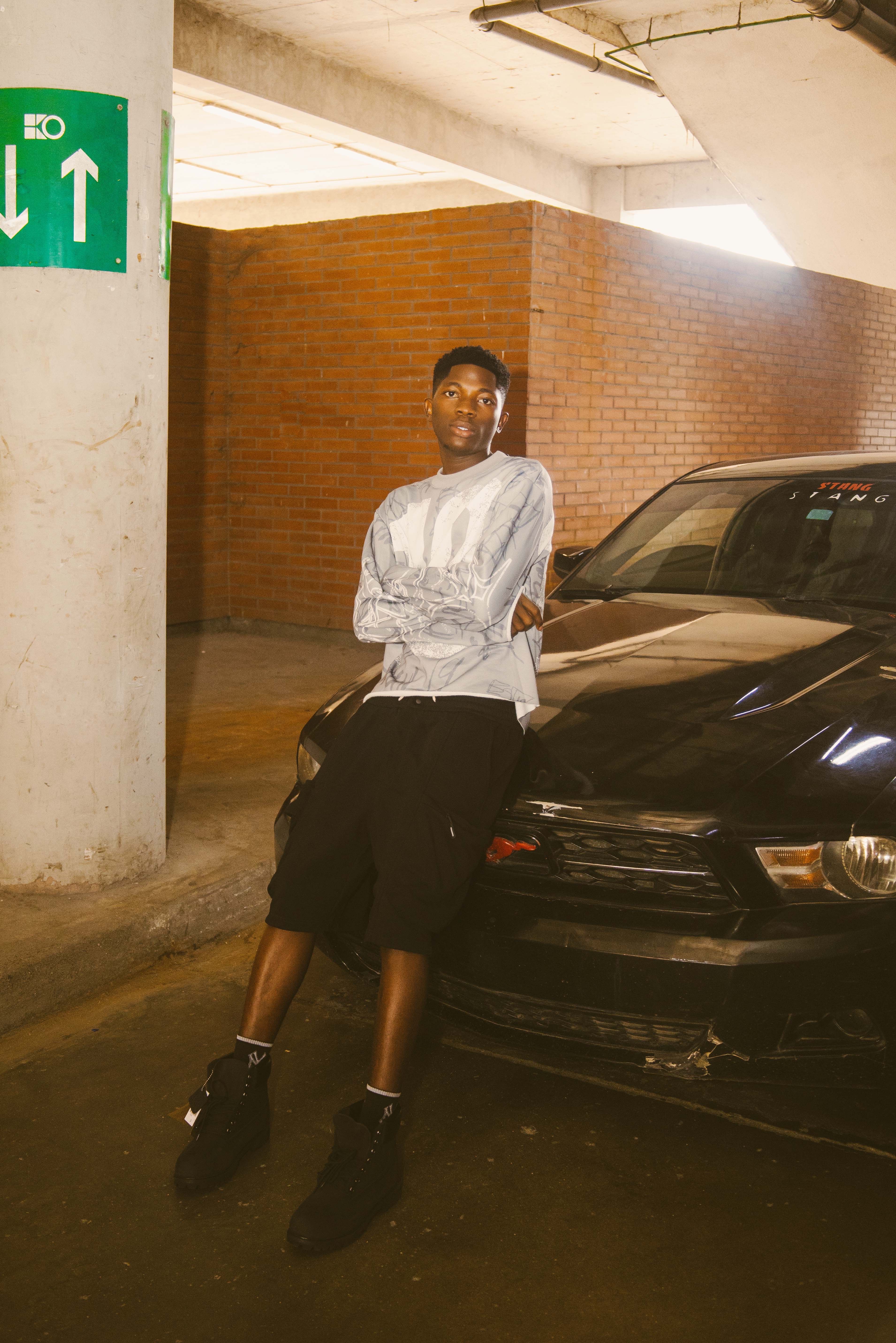 Casual Teenager Relaxing on Car in Urban Garage · Free Stock Photo