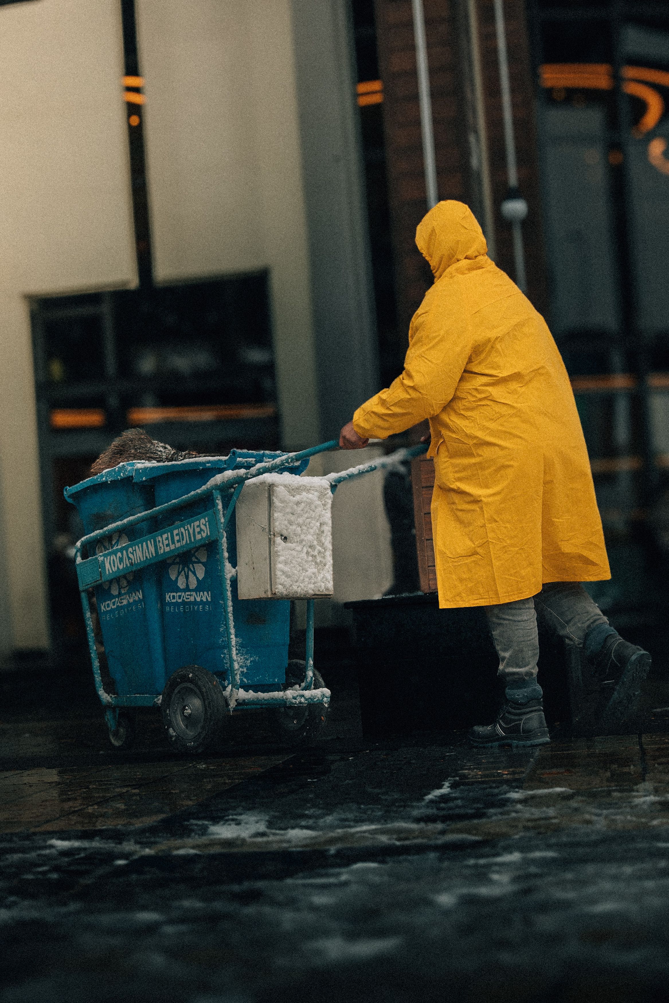 Worker in yellow raincoat carting ice on a rainy day · Free Stock Photo