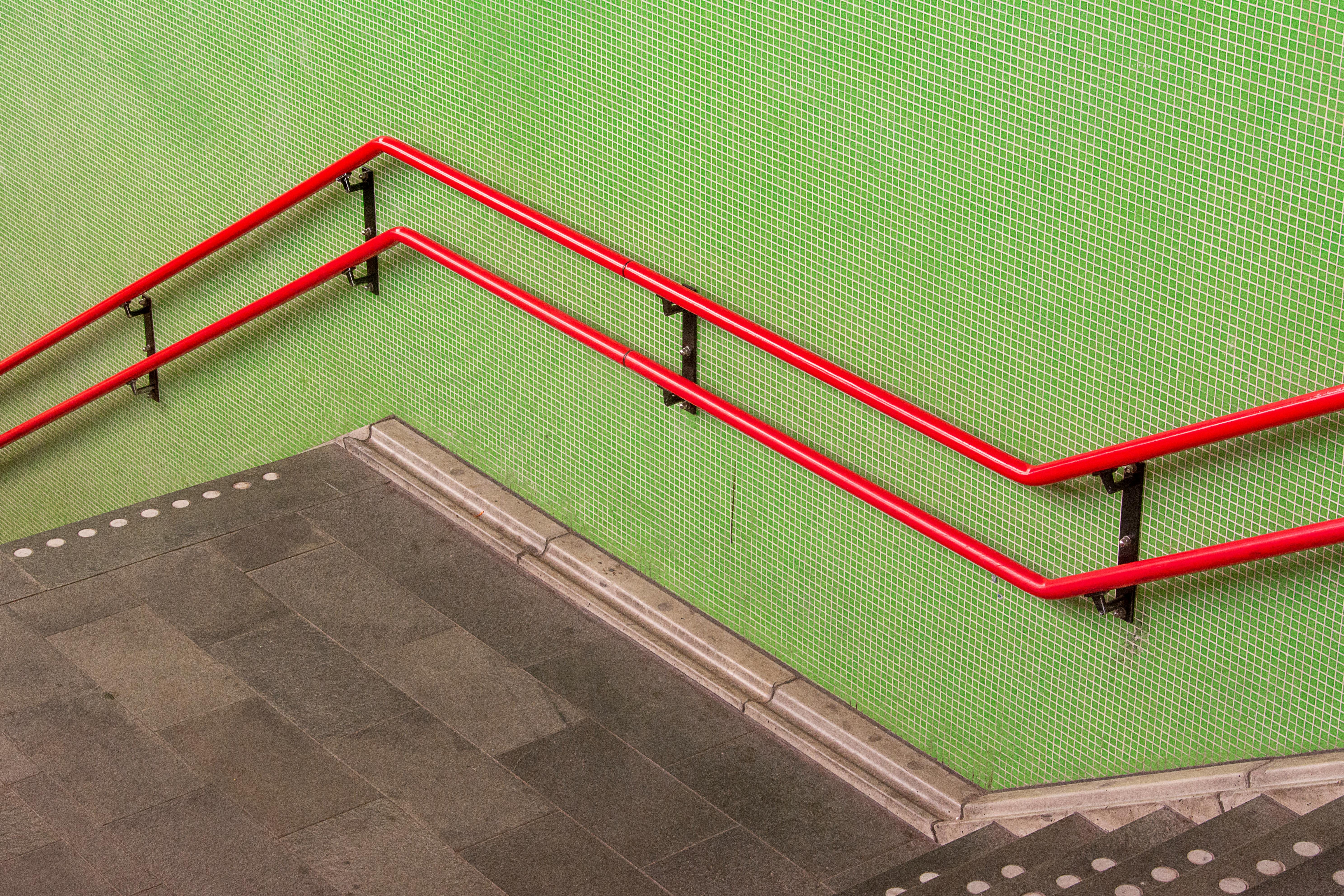 Vibrant Red Handrails Against Green Tiled Wall · Free Stock Photo