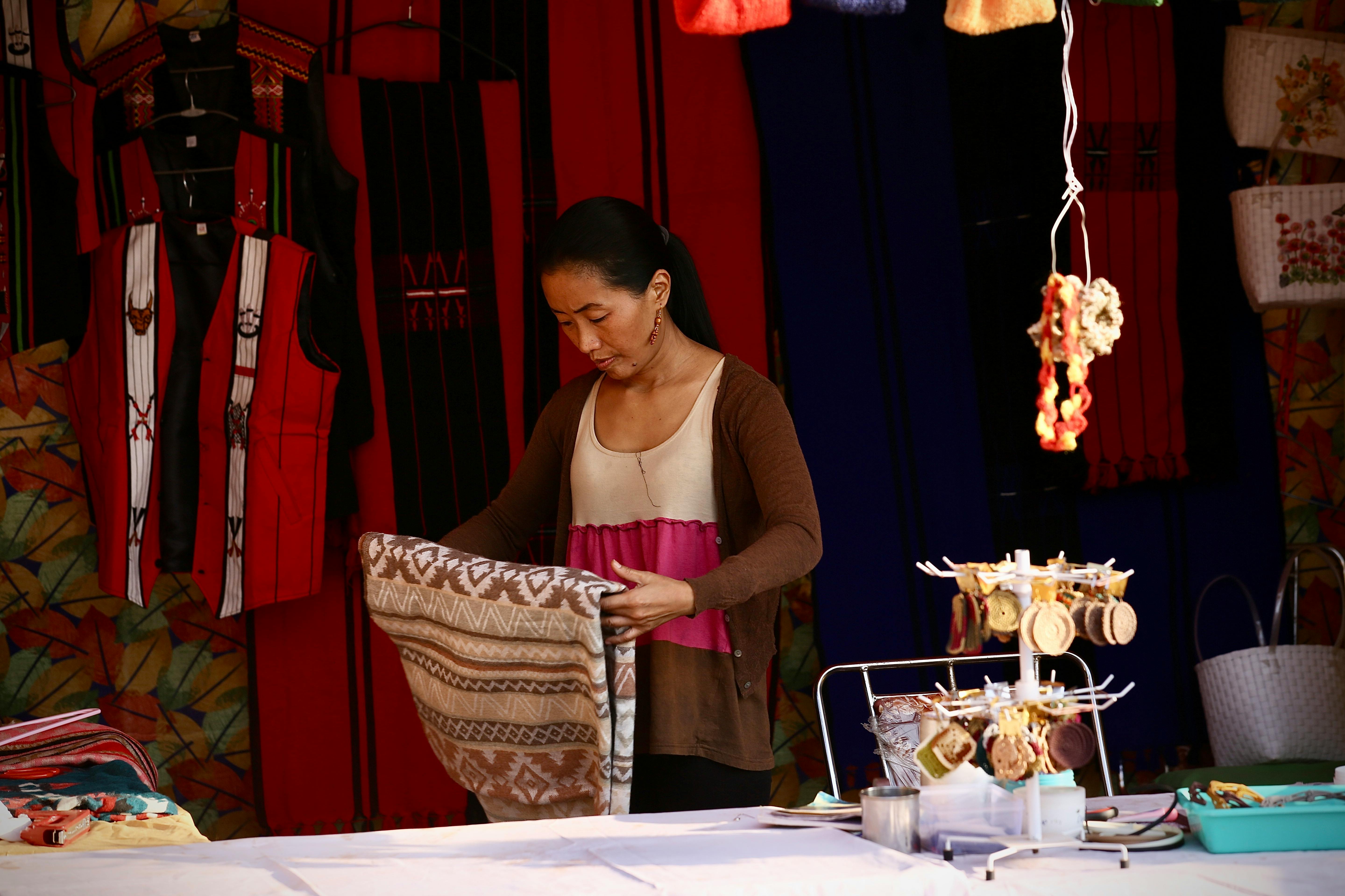 Woman Displaying Traditional Textiles at Market Stall · Free Stock Photo