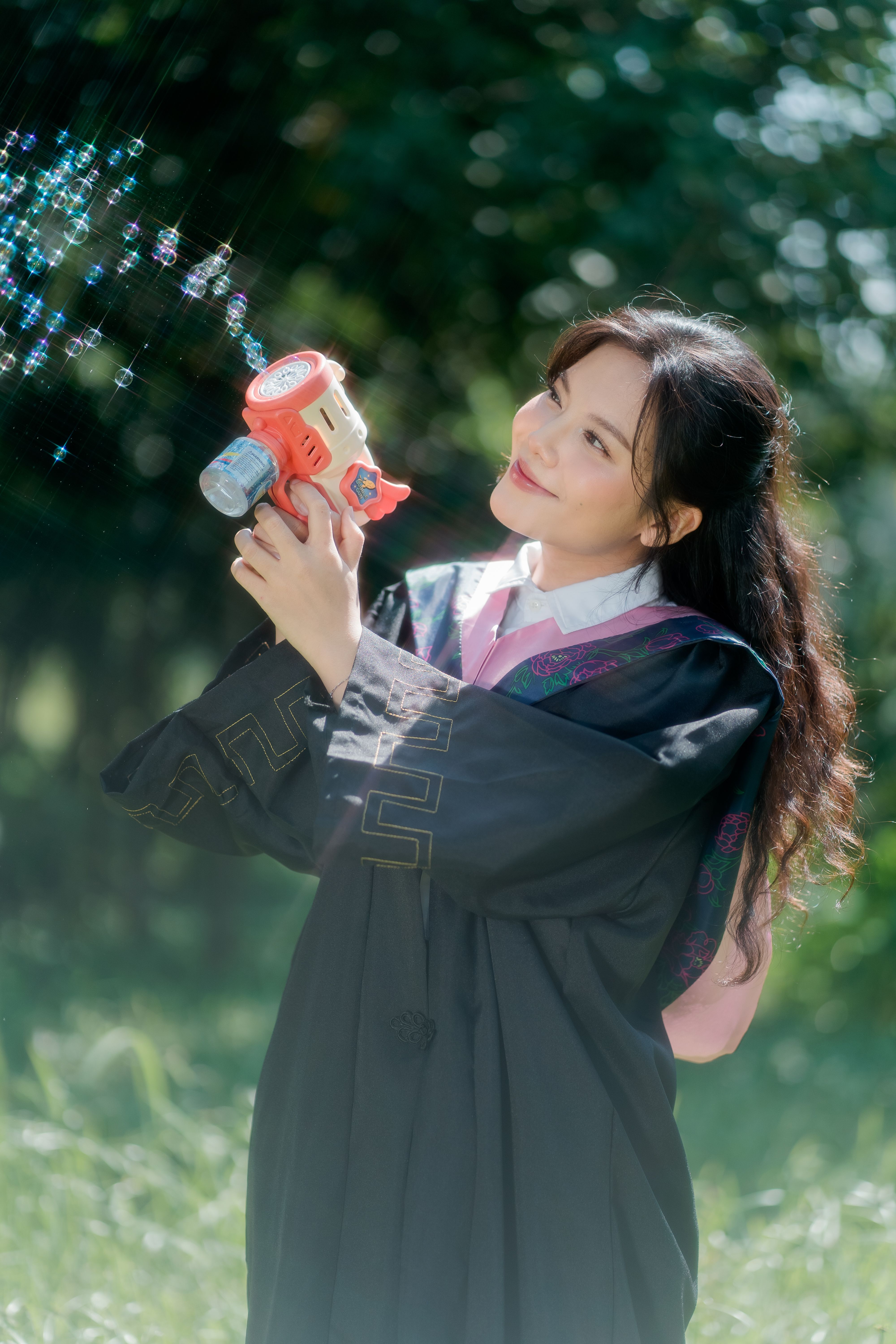 Young Woman in Graduation Gown Blowing Bubbles Outdoors · Free Stock Photo