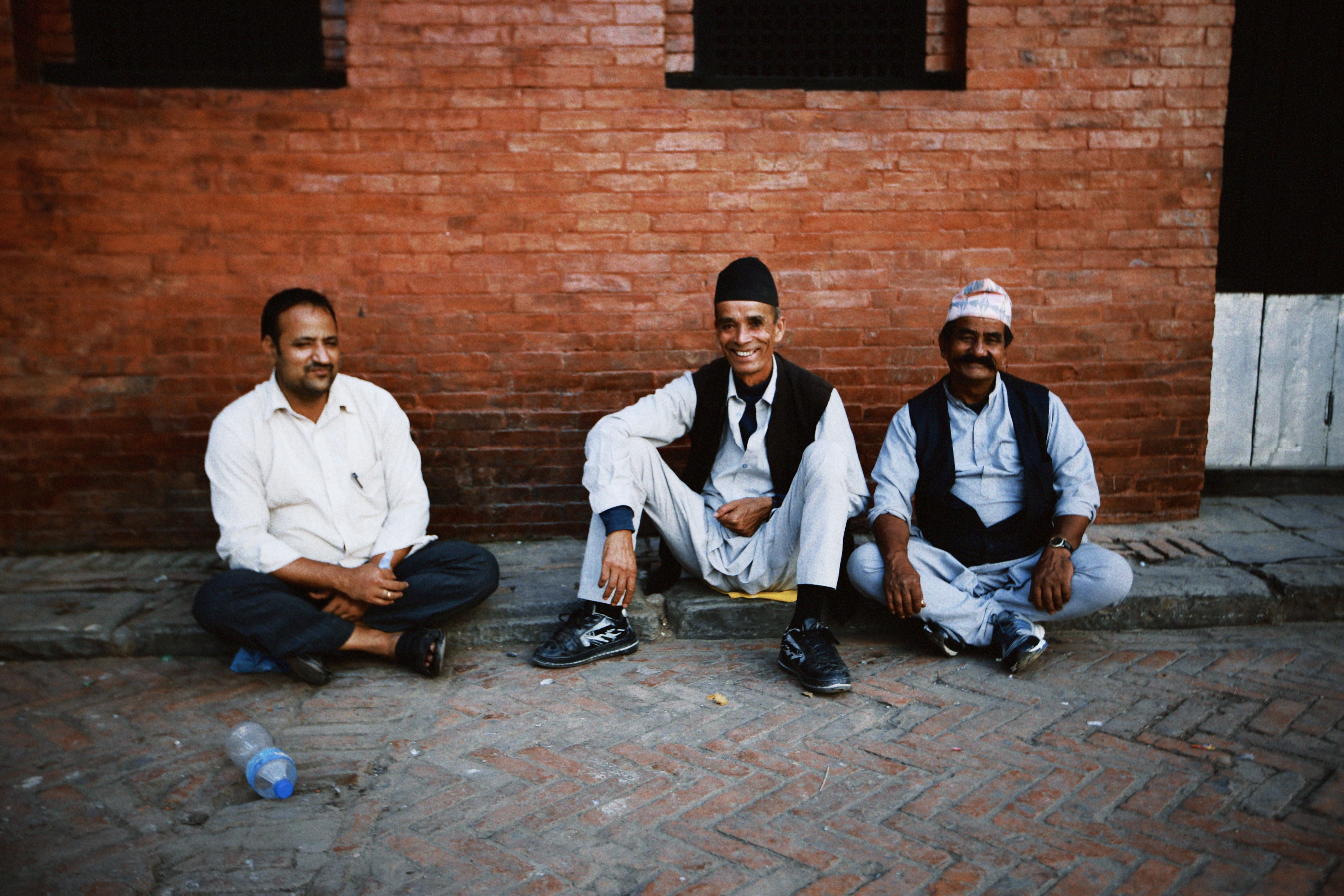 Three Men Sitting Against Red Brick Wall · Free Stock Photo