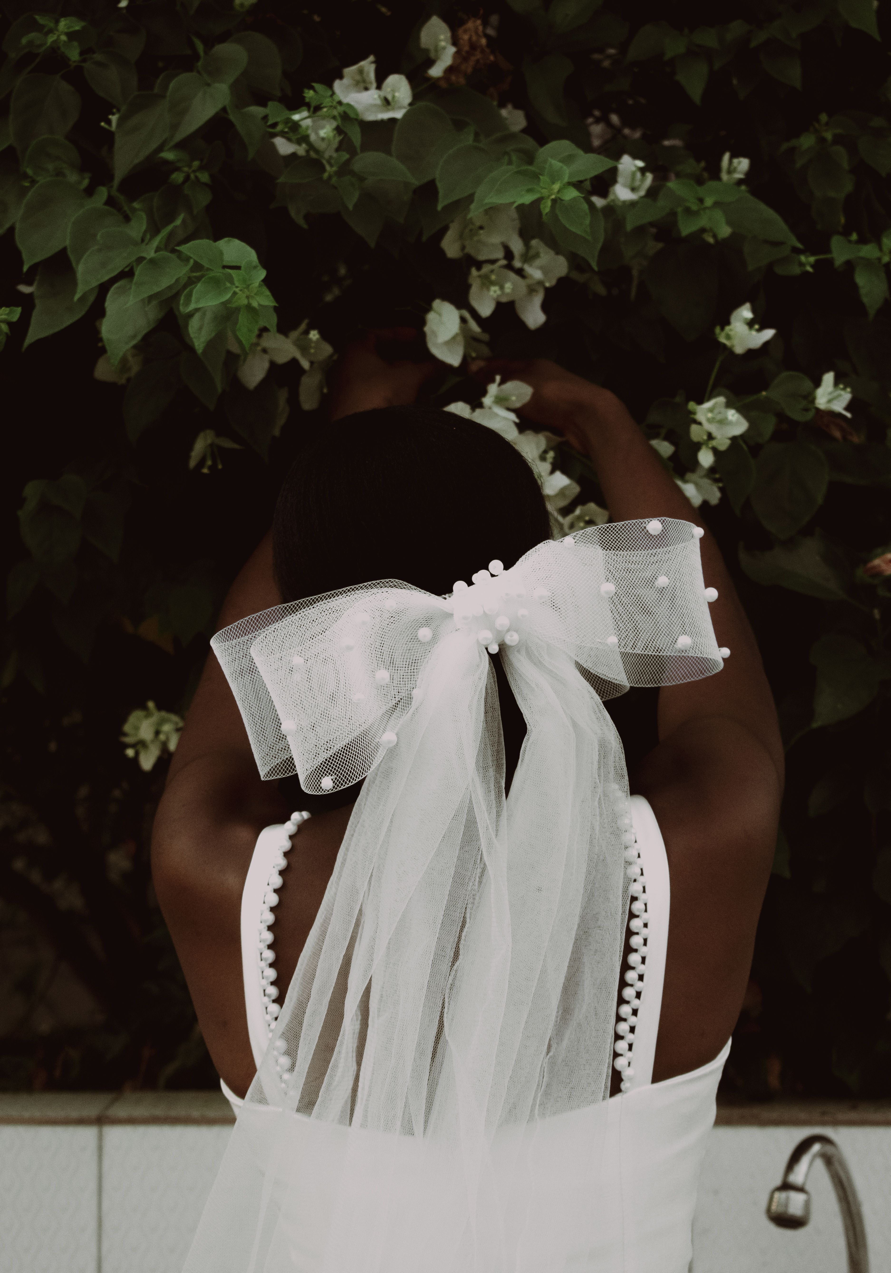 Elegant Bride with Lace Bow Reaching for Flowers · Free Stock Photo