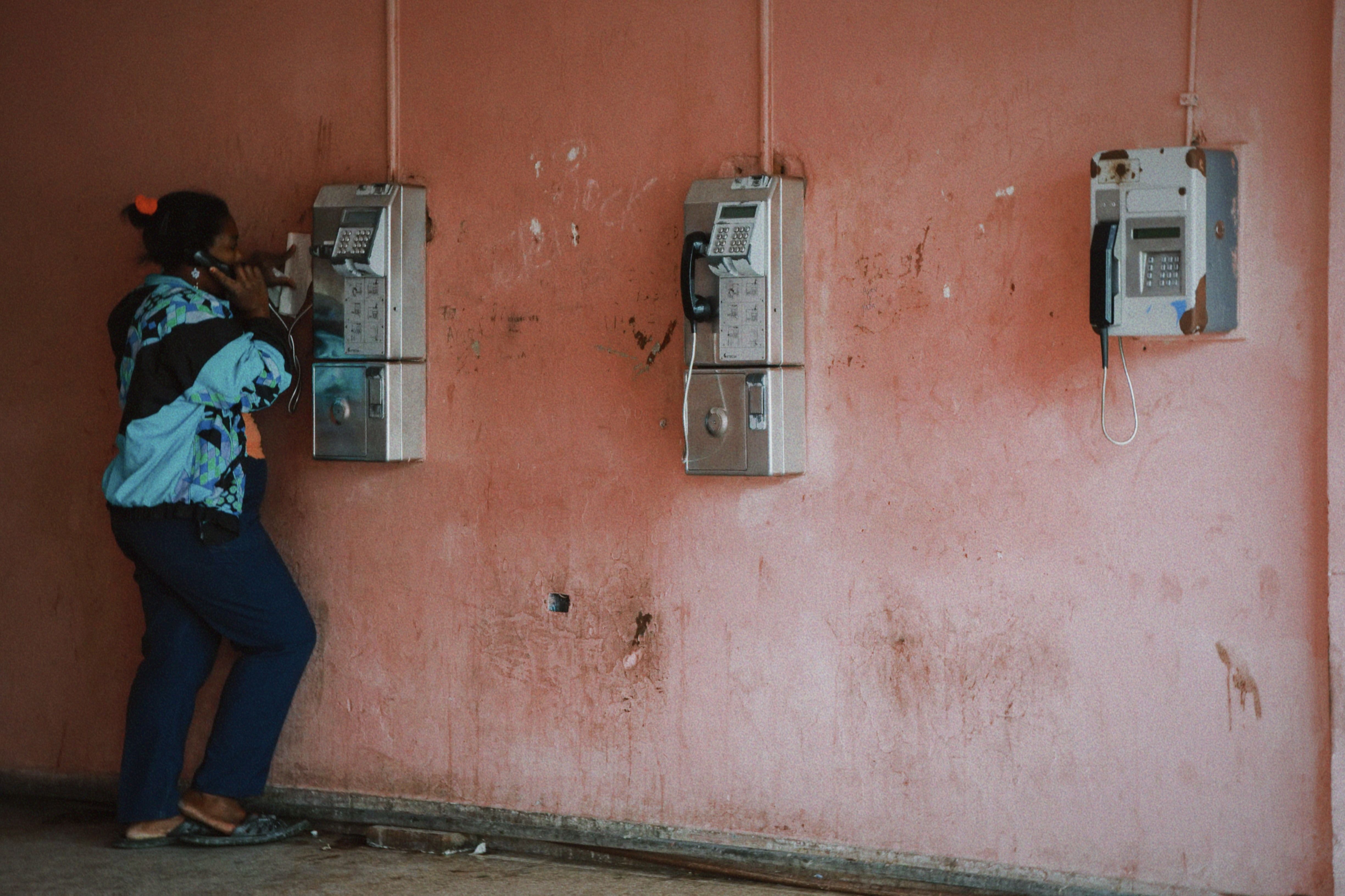 Woman Using Public Payphones Against Worn Wall · Free Stock Photo