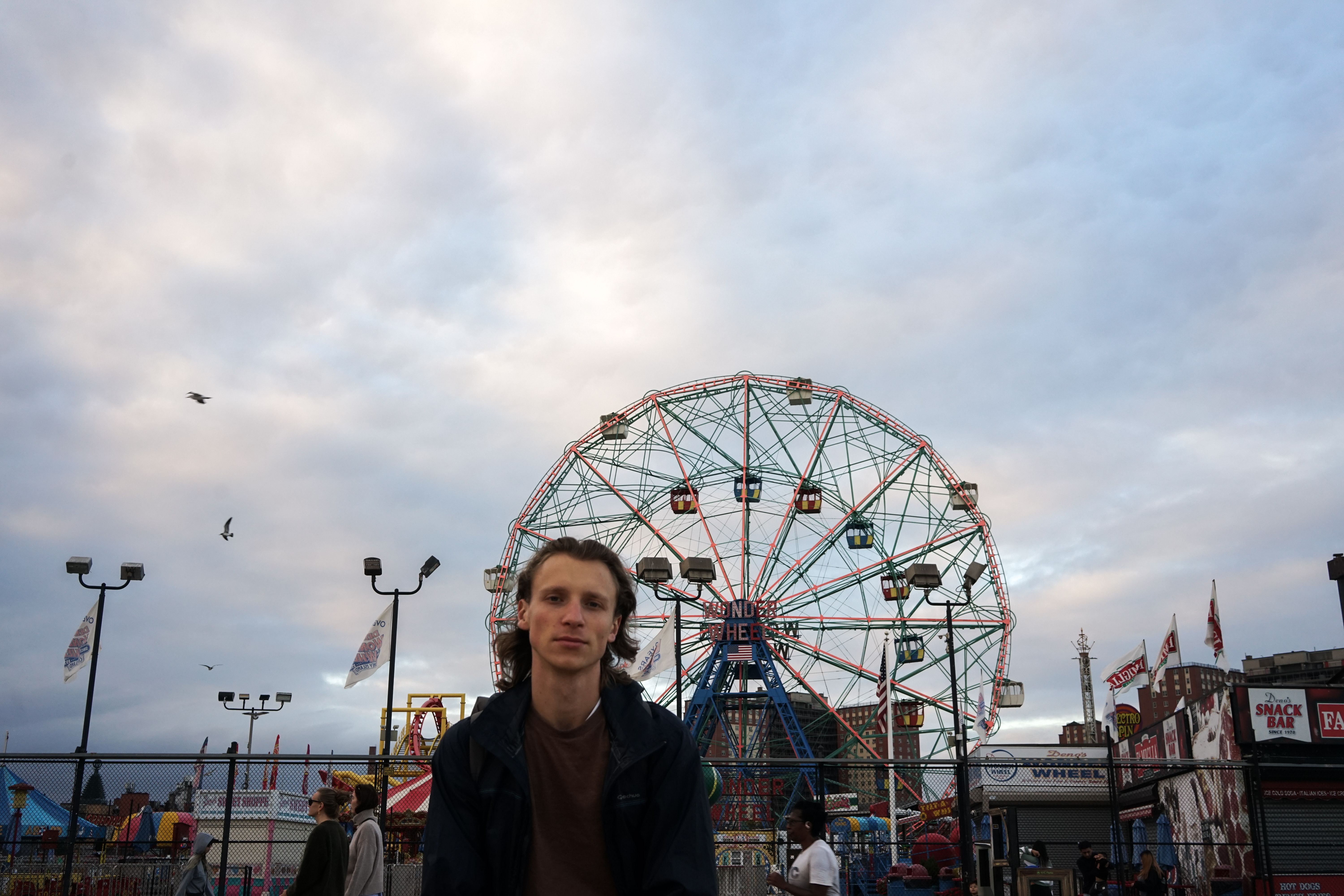 Young Man at Amusement Park with Ferris Wheel · Free Stock Photo