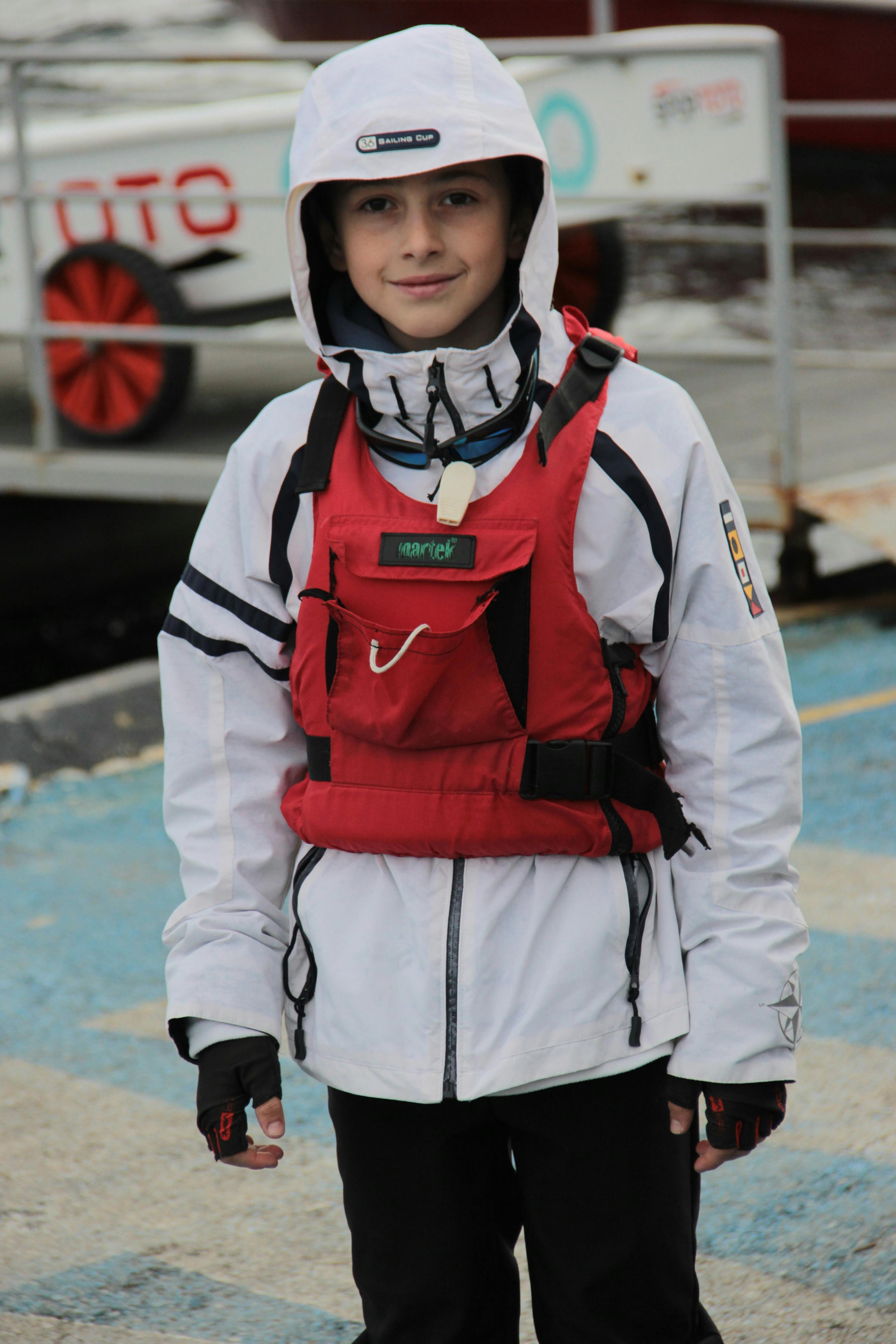 Young Boy in White Jacket and Red Life Vest at Marina · Free Stock Photo