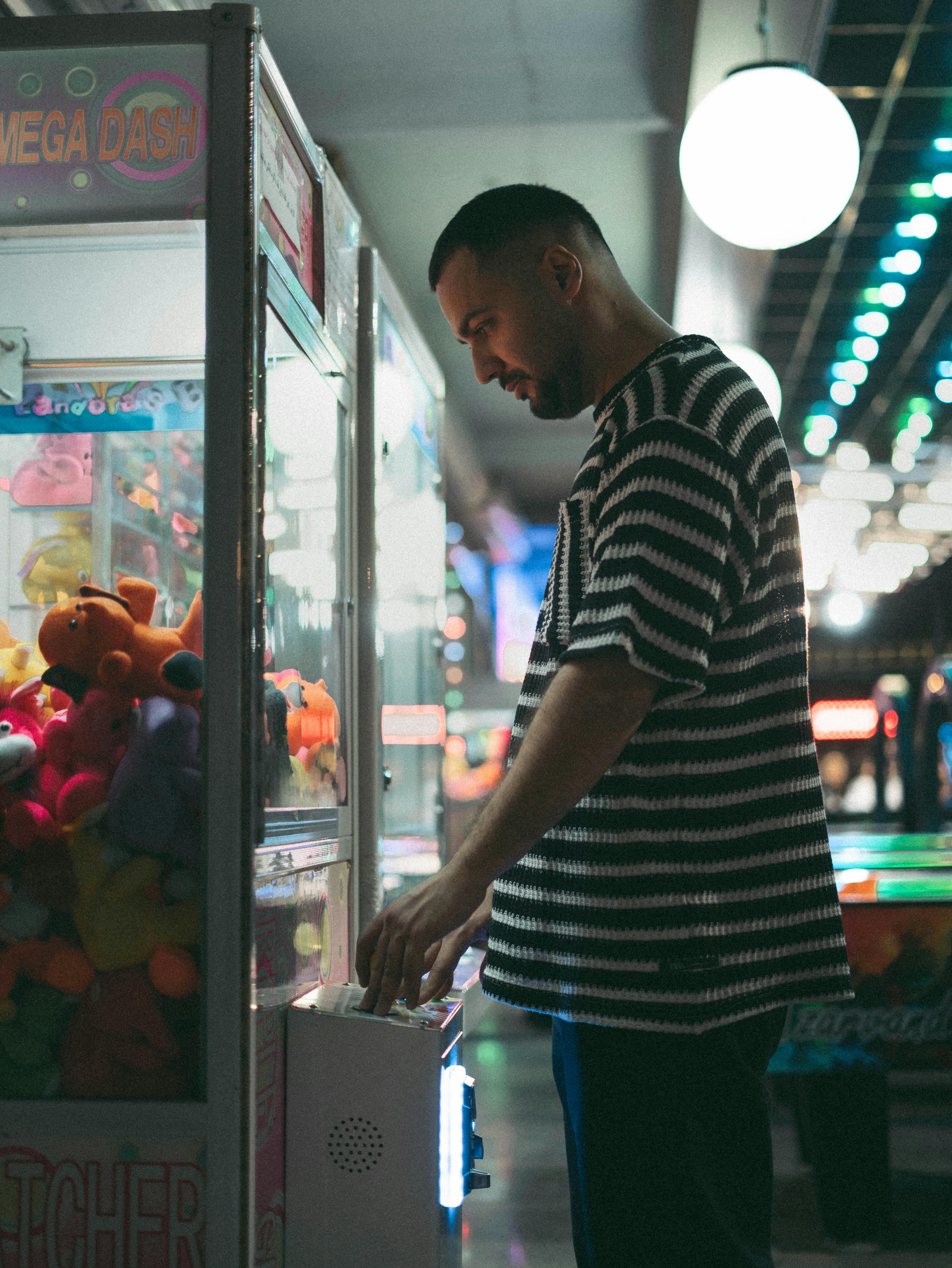Man Playing Claw Machine in Neon-lit Arcade · Free Stock Photo