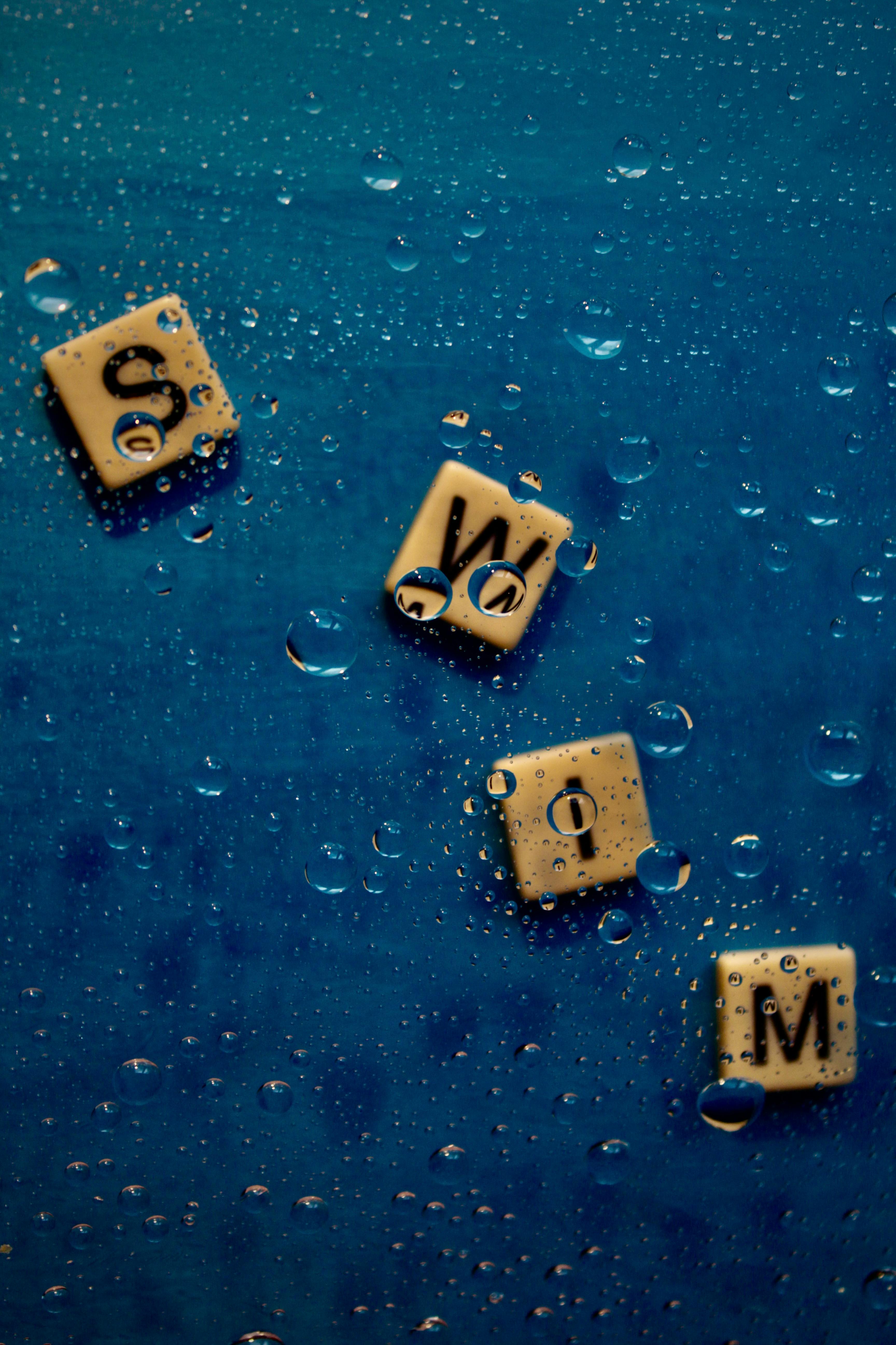 Wet Scrabble Tiles on Blue Surface · Free Stock Photo