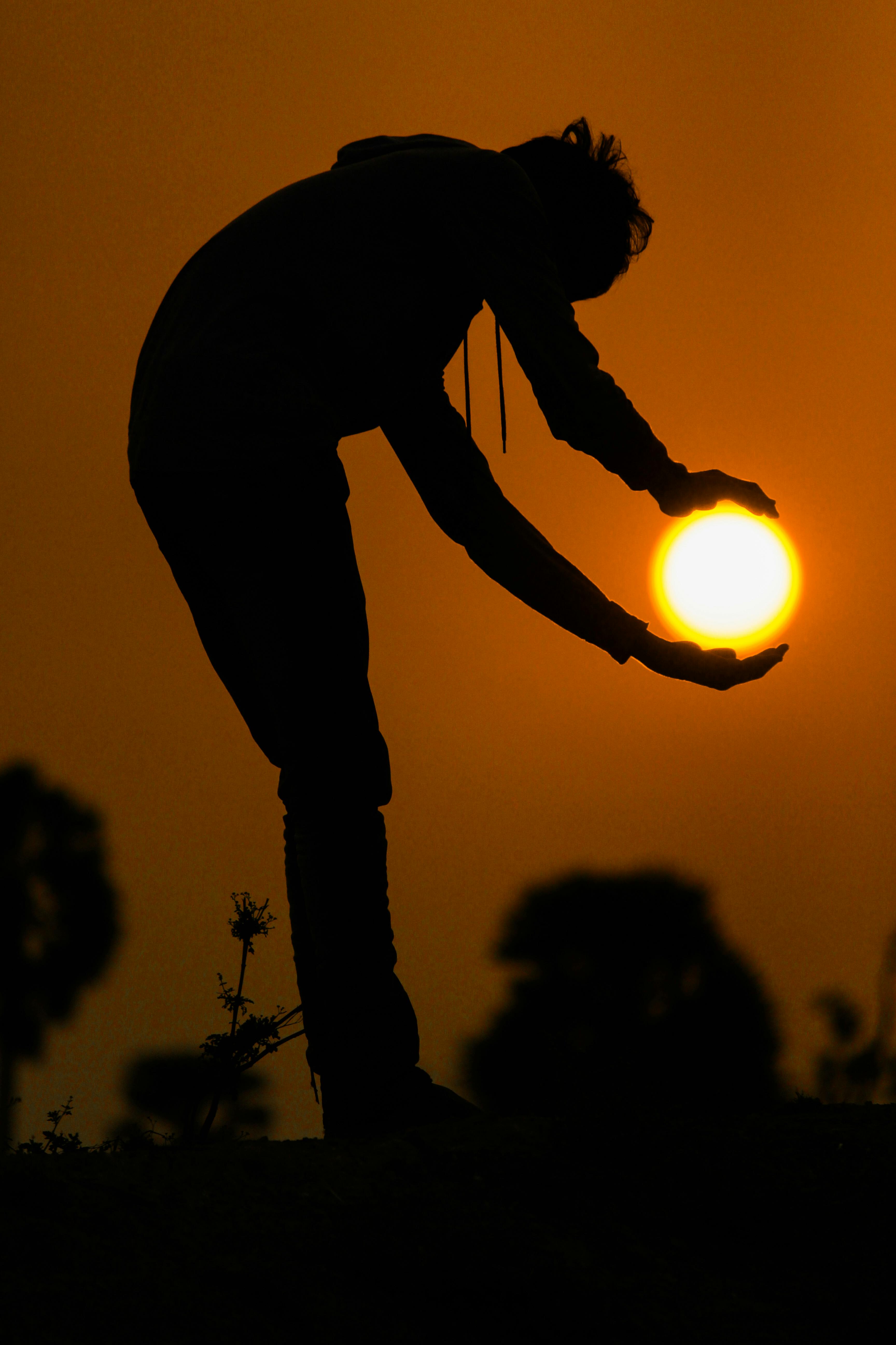 Silhouette of Person Holding Sun at Sunset · Free Stock Photo