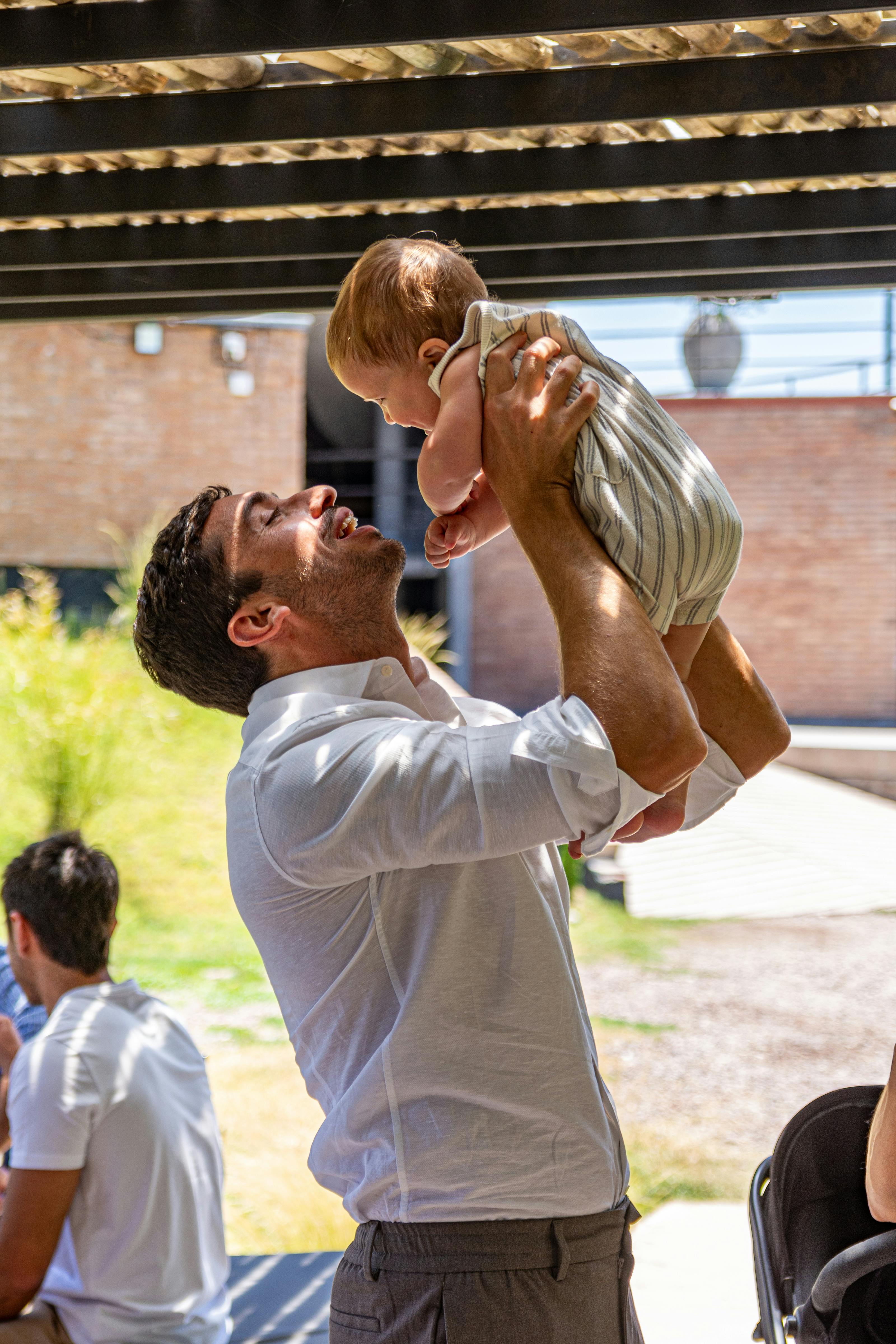 Joyful Father Lifting Baby Outdoors on a Sunny Day · Free Stock Photo