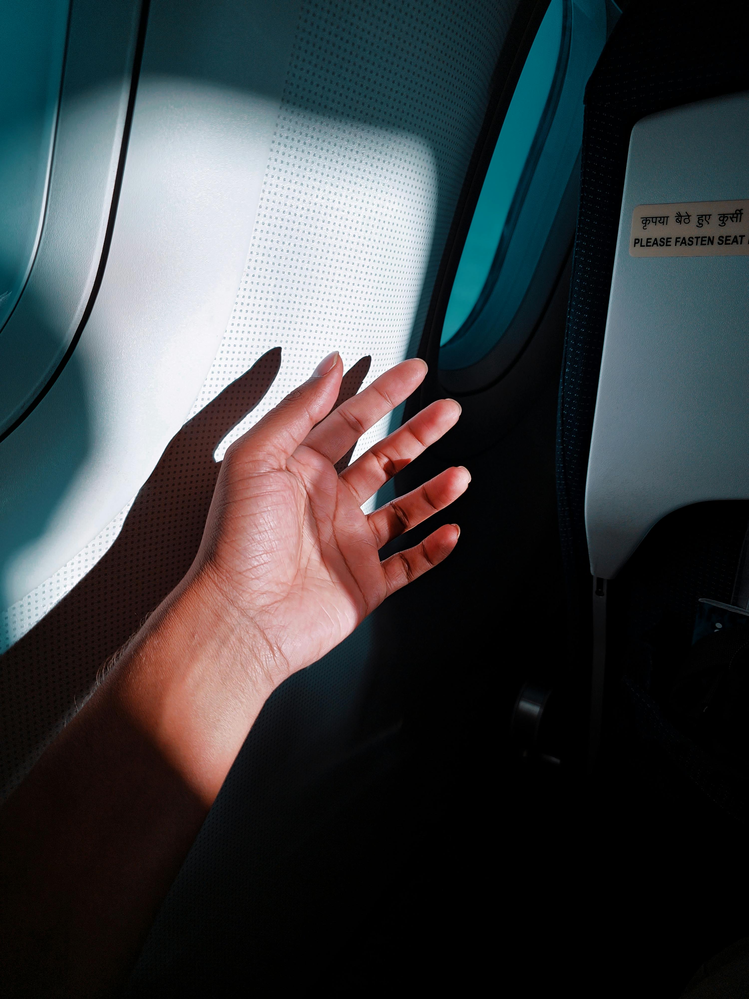 Hand Reaching Toward Airplane Window Light · Free Stock Photo