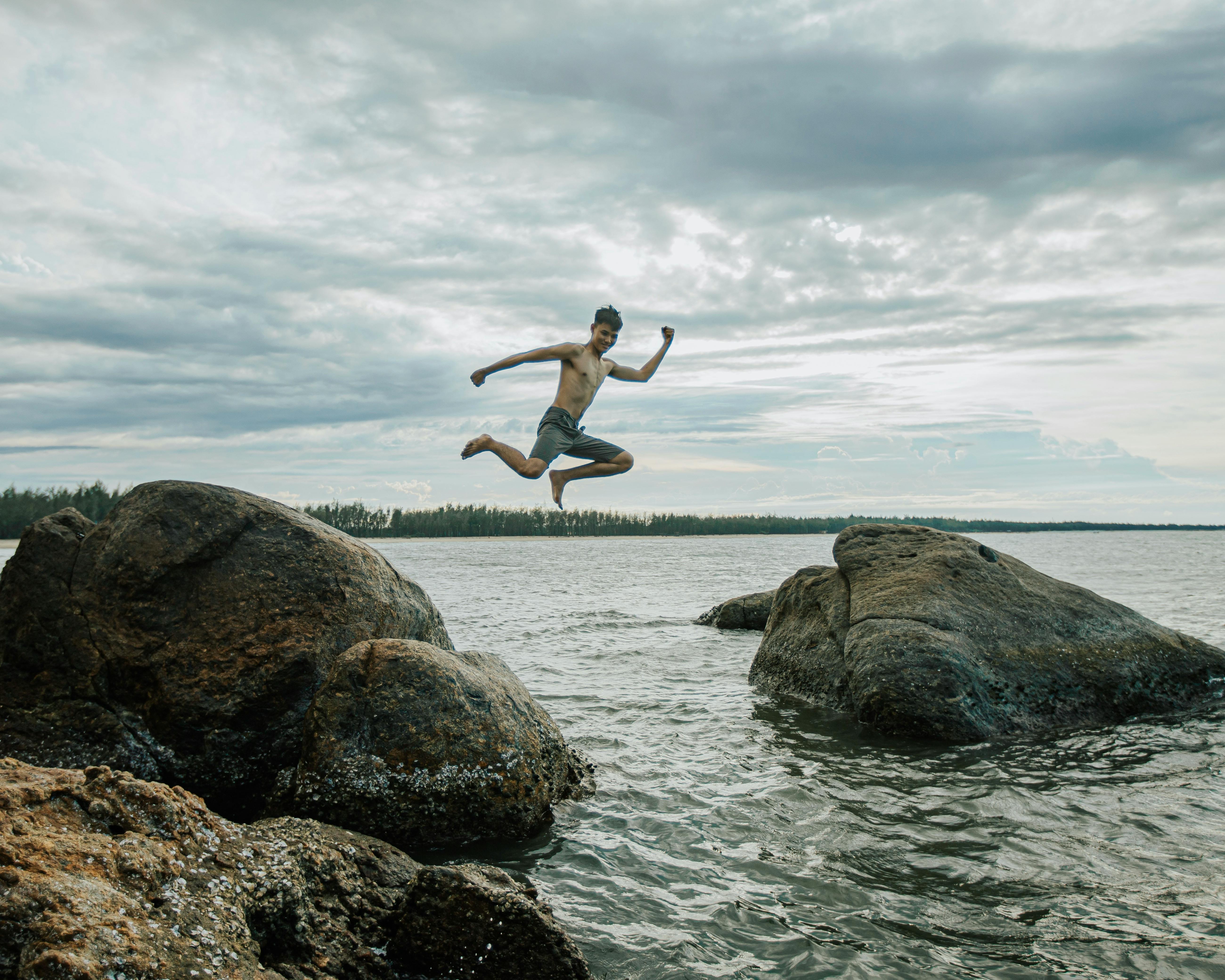 Young man jumping between rocks at seaside · Free Stock Photo