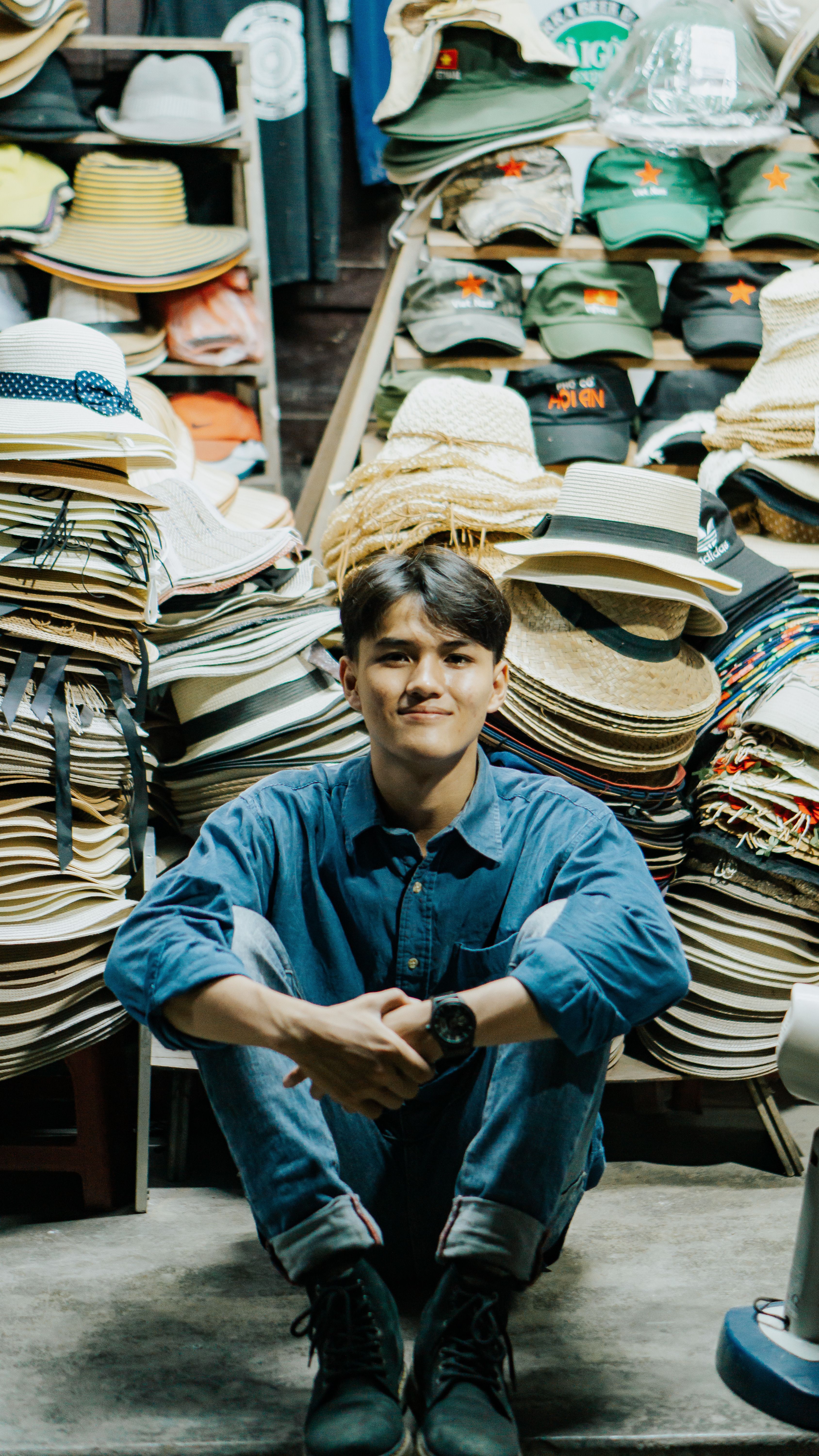 Young Man Sitting in Hat Store Surrounded by Hats · Free Stock Photo