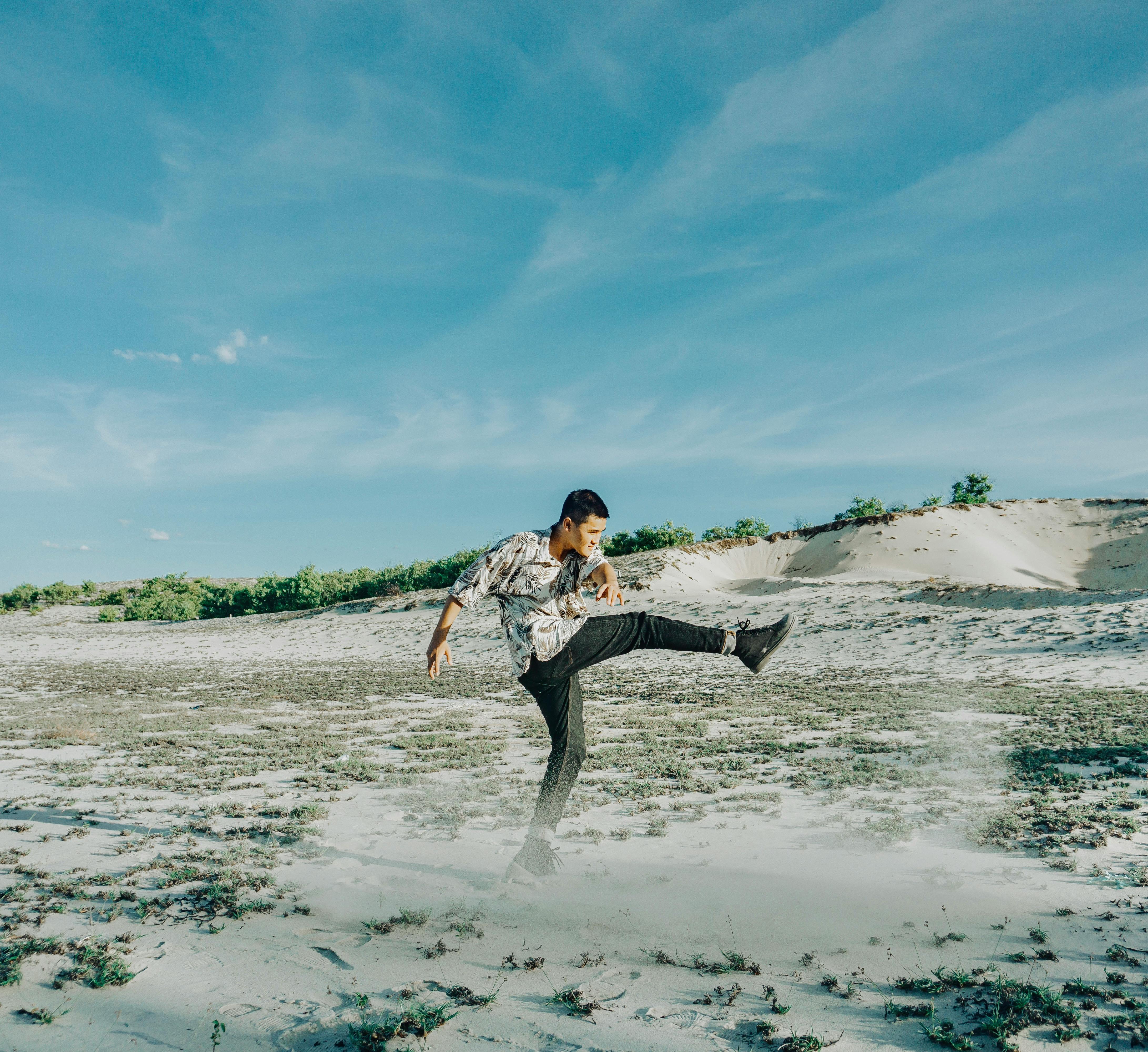Man Kicking Sand in Desert Landscape Under Blue Sky · Free Stock Photo