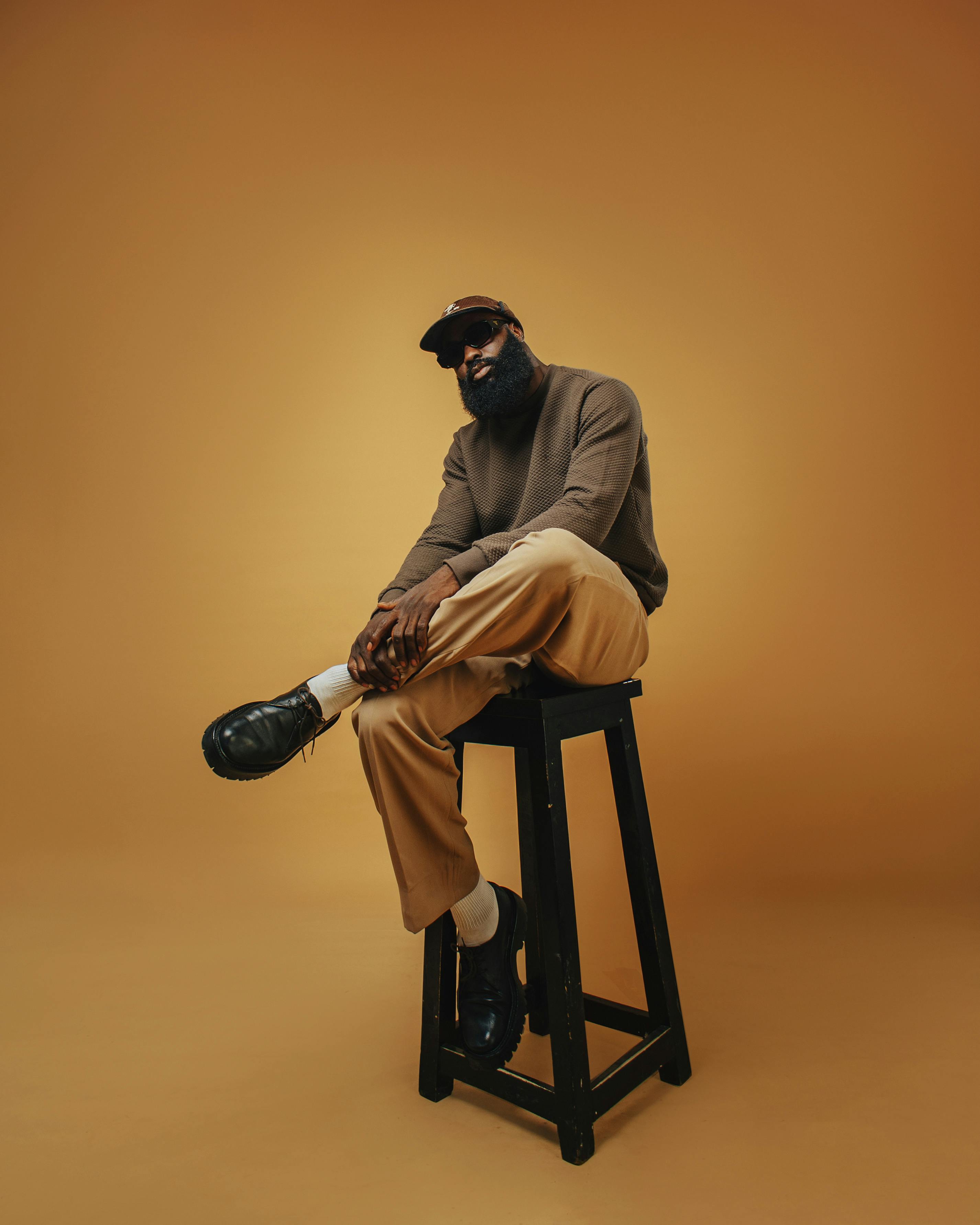 Stylish man posing on stool with warm backdrop · Free Stock Photo