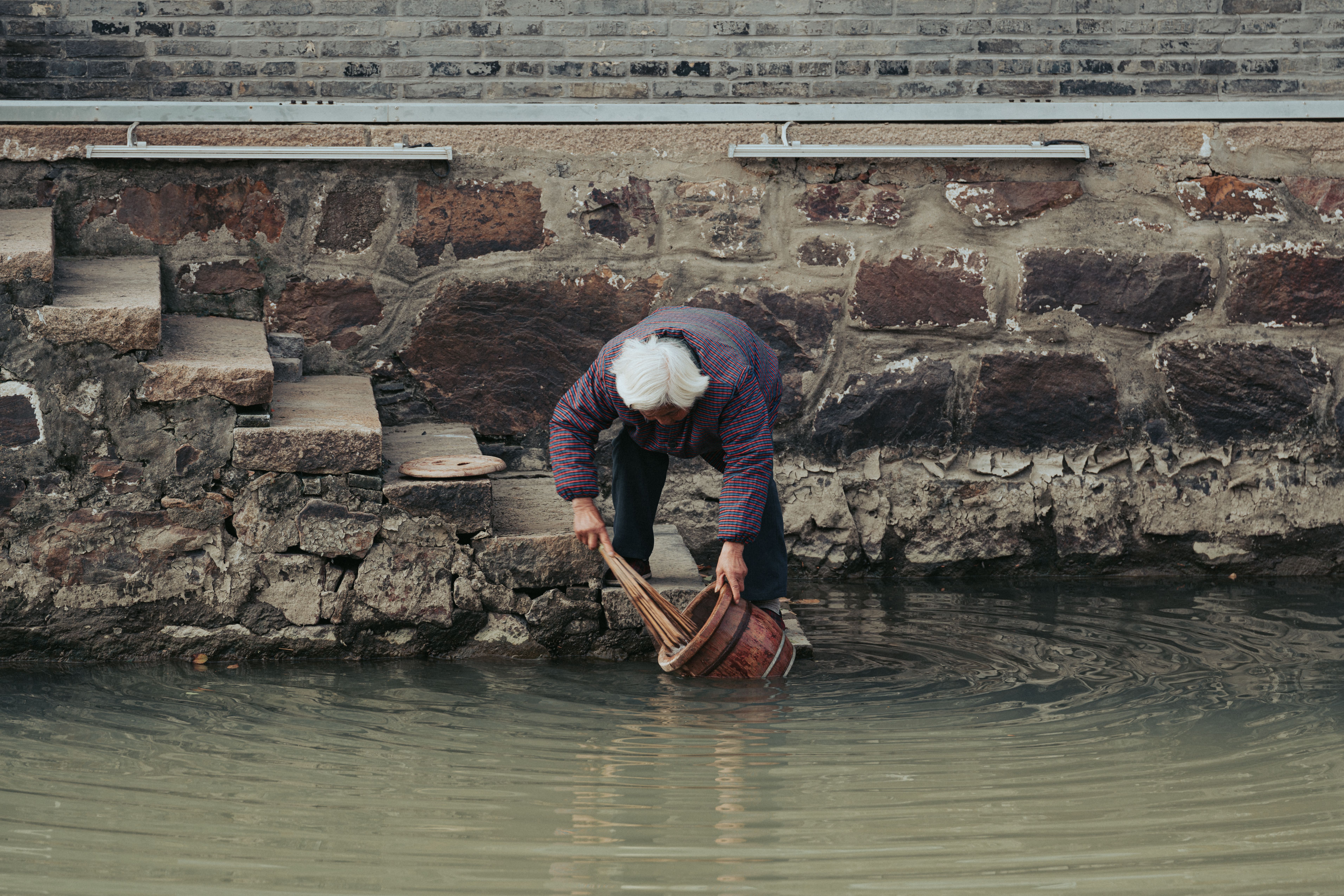 Elderly Person Collecting Water by Stone Wall · Free Stock Photo
