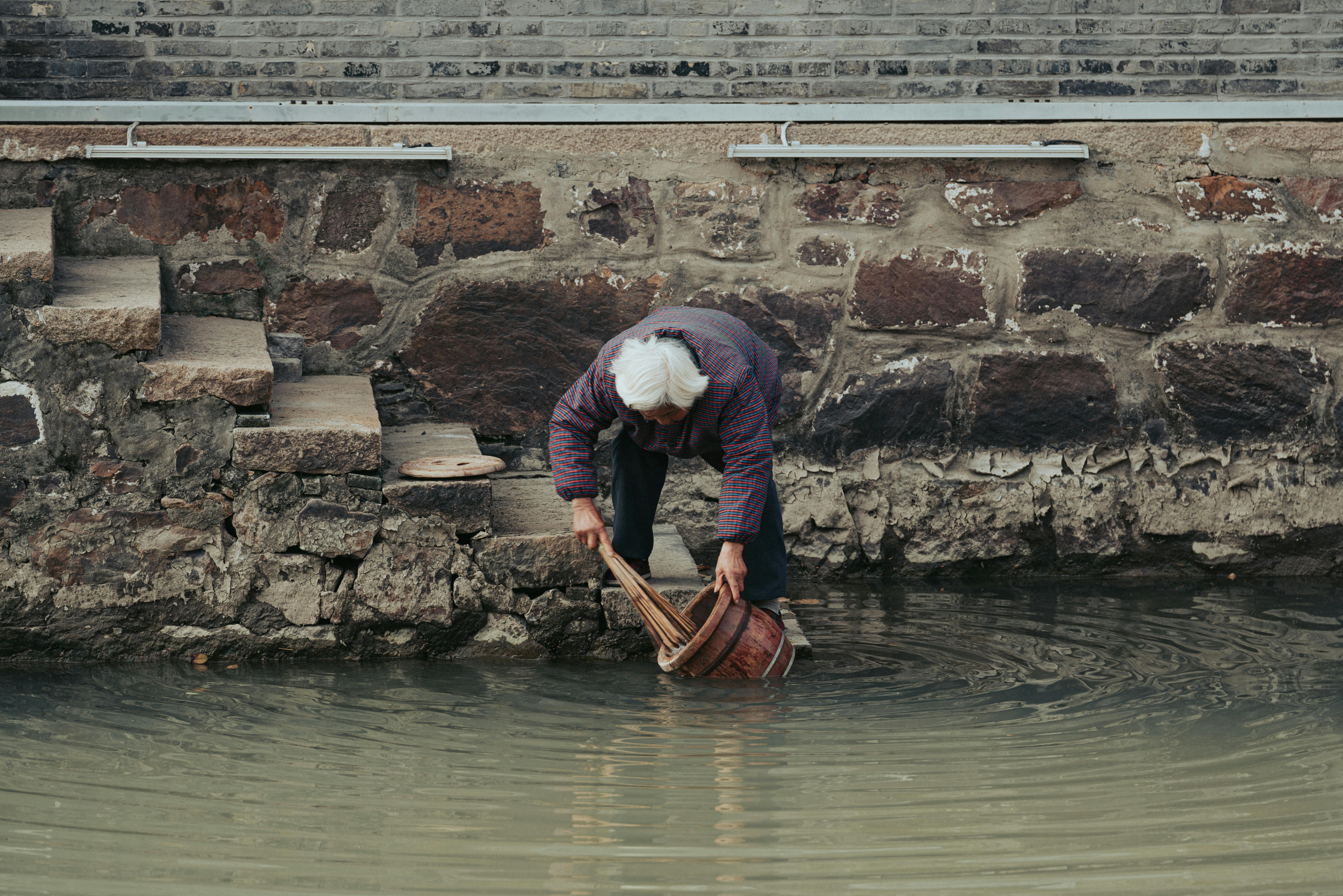 Persona Mayor Recogiendo Agua Junto A Un Muro De Piedra · Foto de stock ...