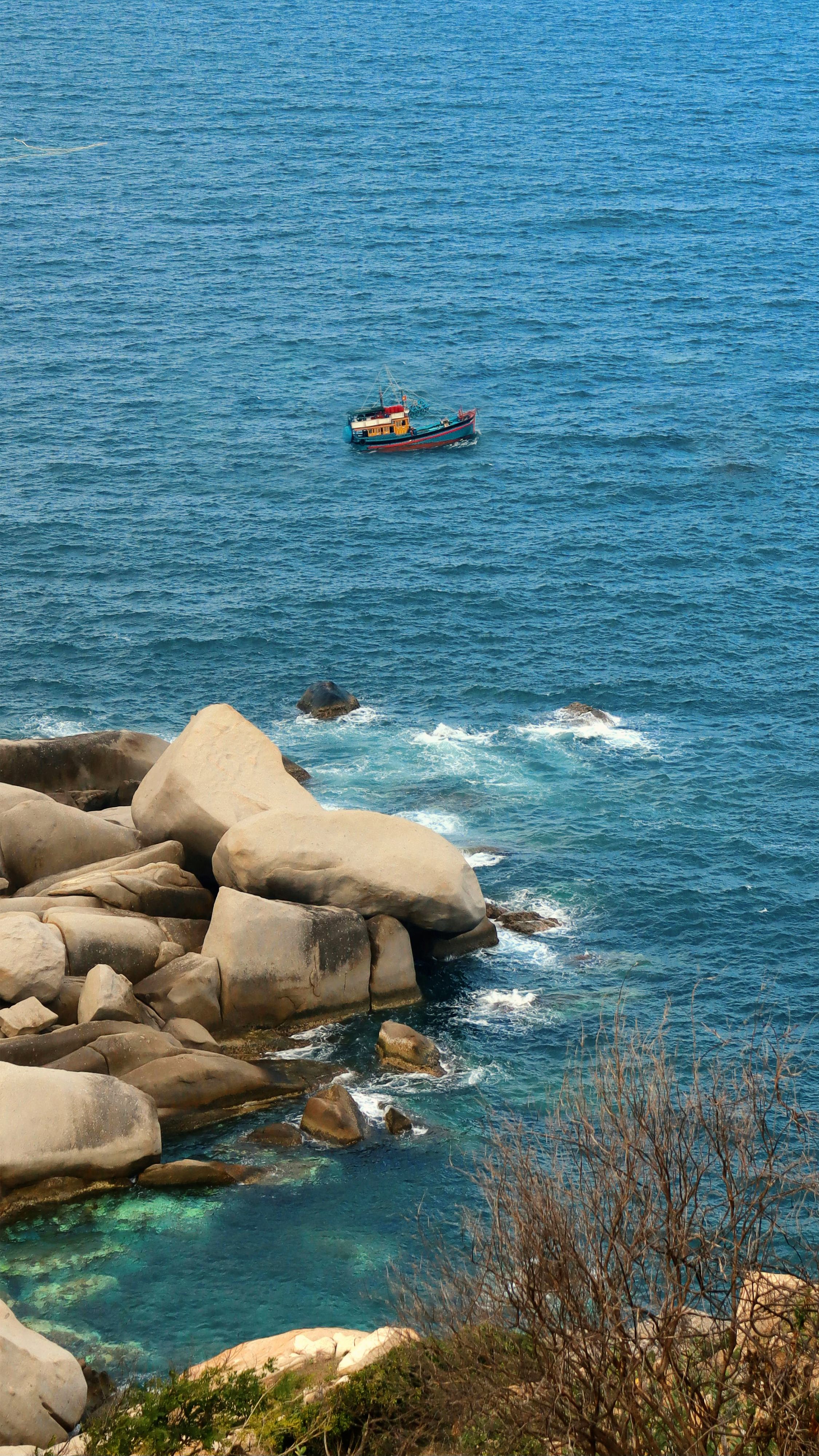Colorful Boat Sailing on Rocky Shoreline · Free Stock Photo