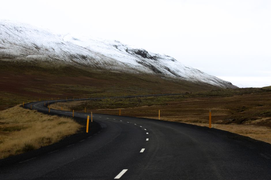 Winding road in Iceland with snow-covered mountains and open landscape, ideal for travel inspiration.