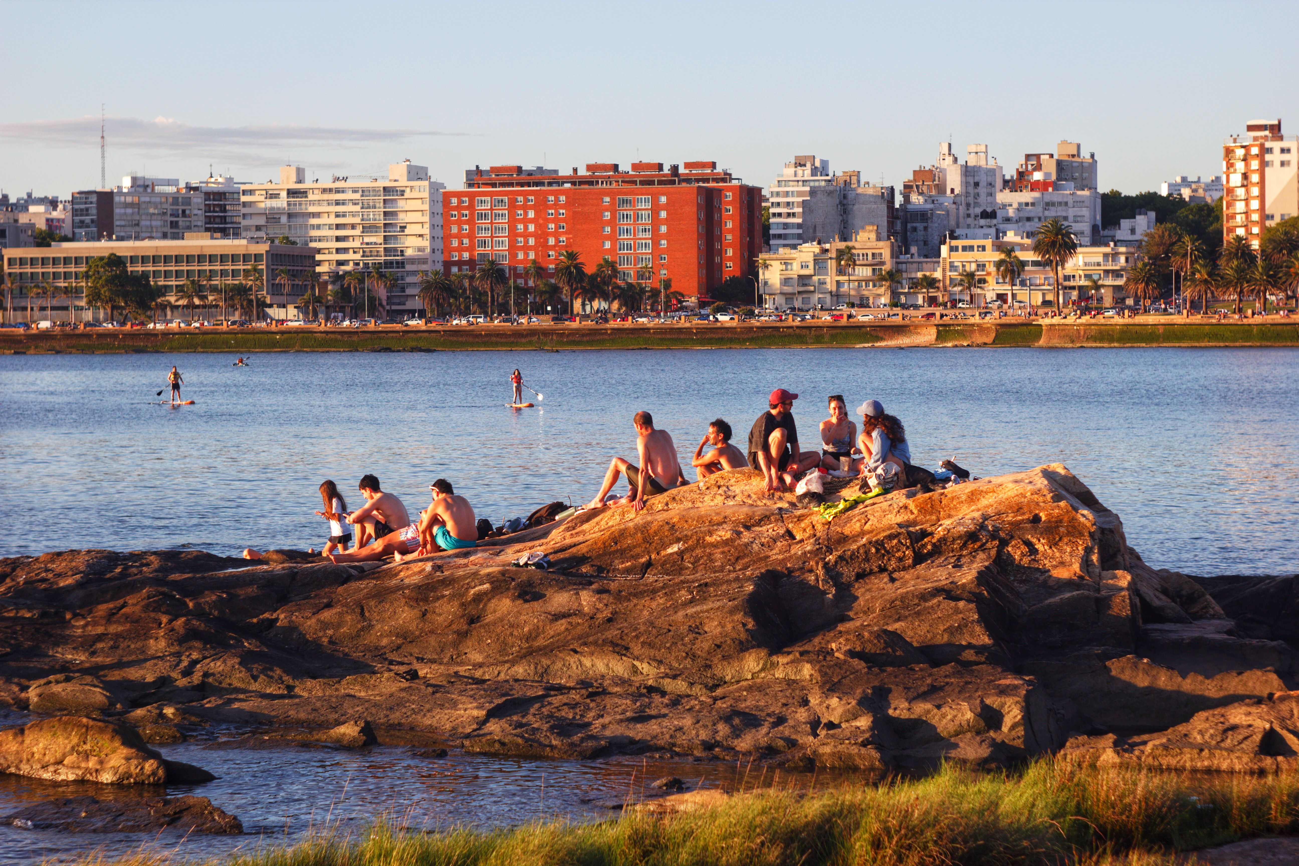 People Relaxing on Rocks by the Riverside Cityscape · Free Stock Photo