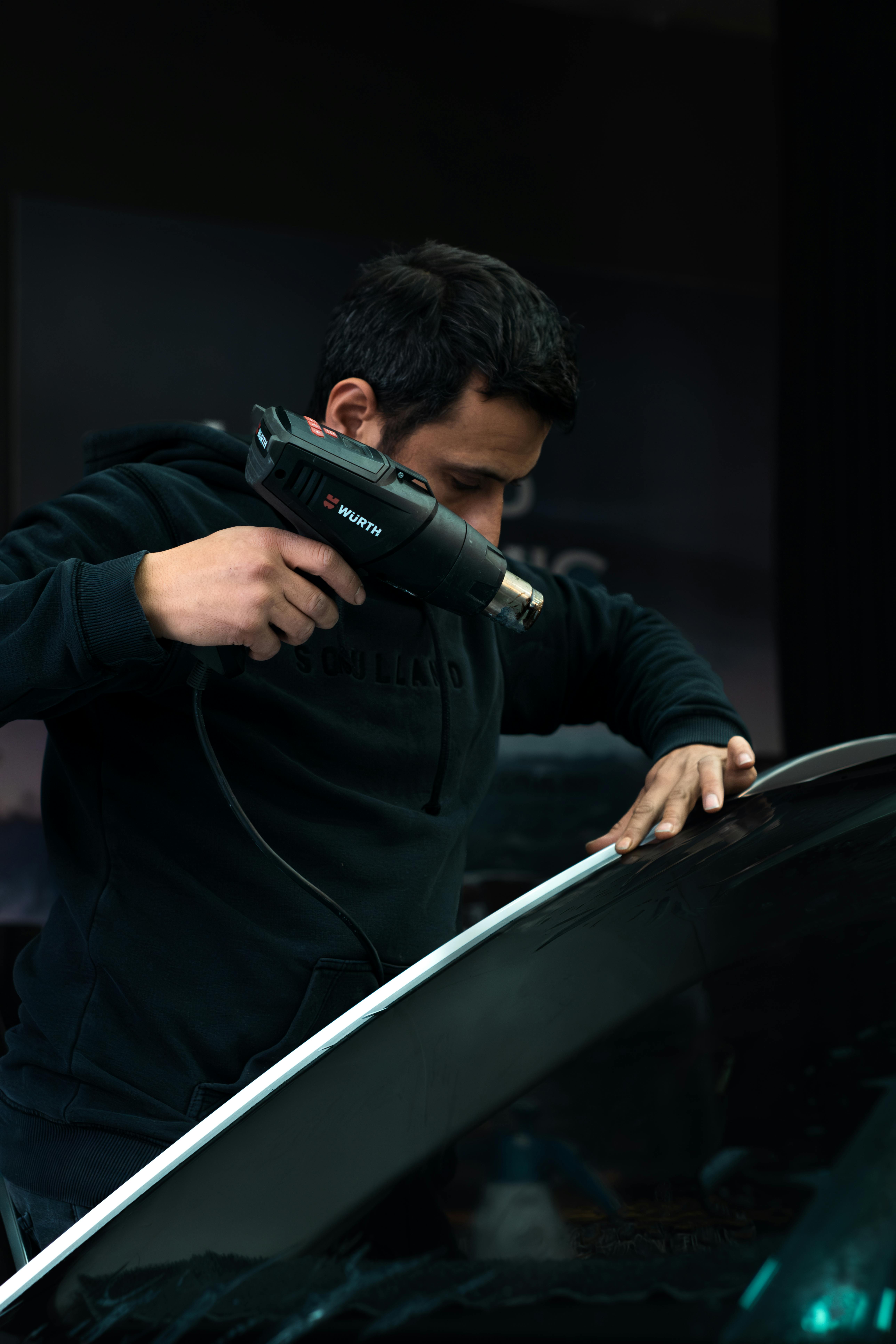 Man Using Heat Gun on Car Windshield Indoors · Free Stock Photo