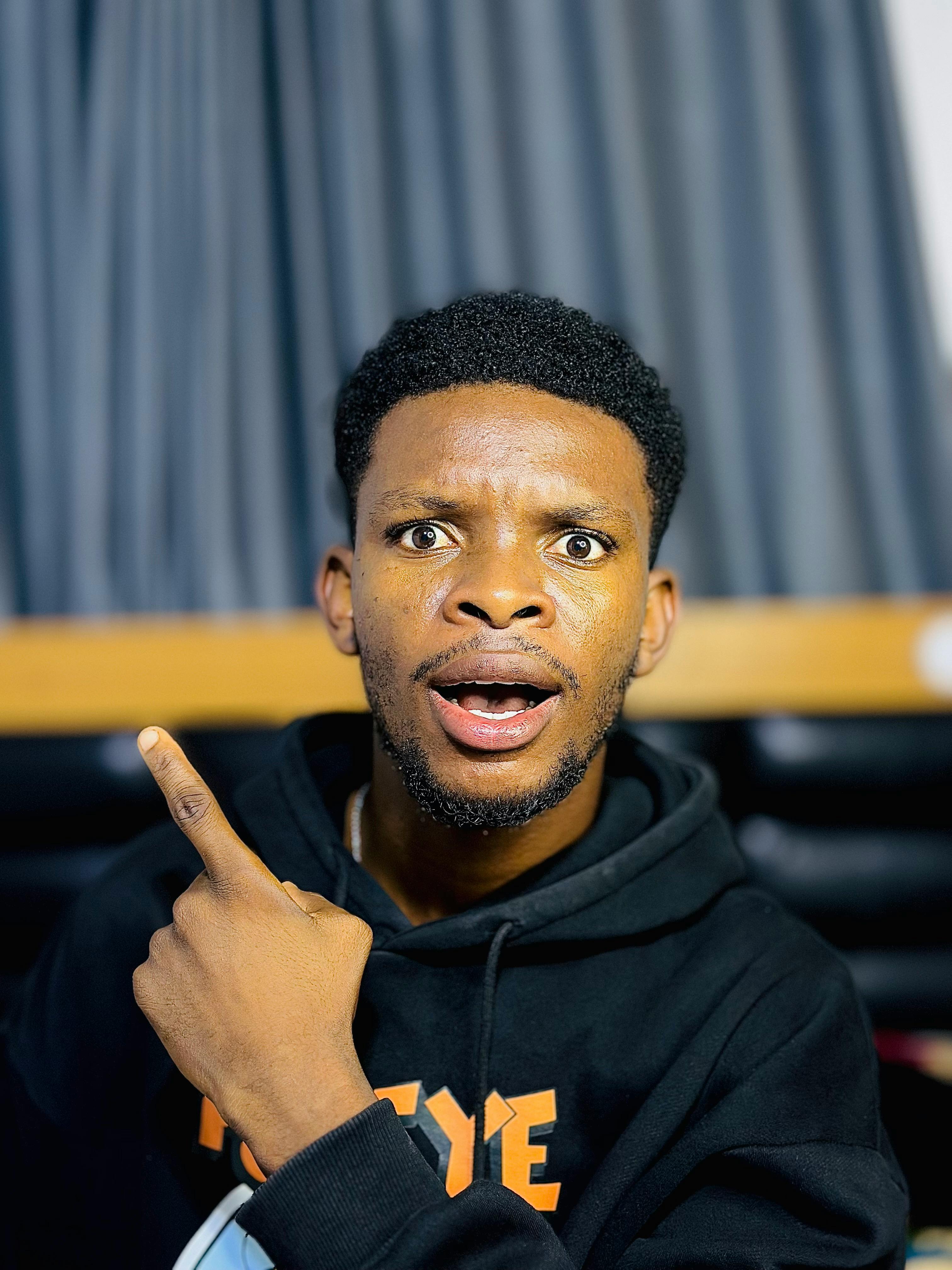 Surprised Young Man Pointing Indoors · Free Stock Photo