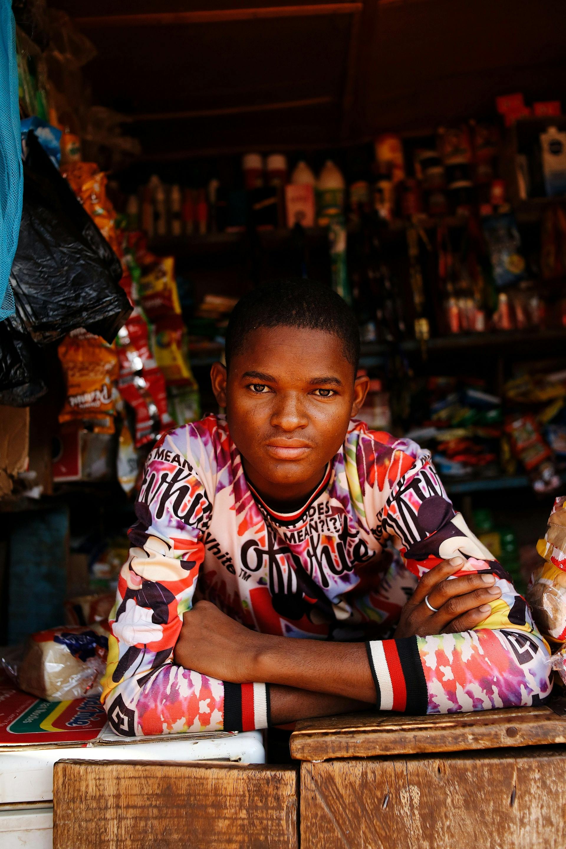 Young Man in Vibrant Shirt at Nigerian Storefront · Free Stock Photo