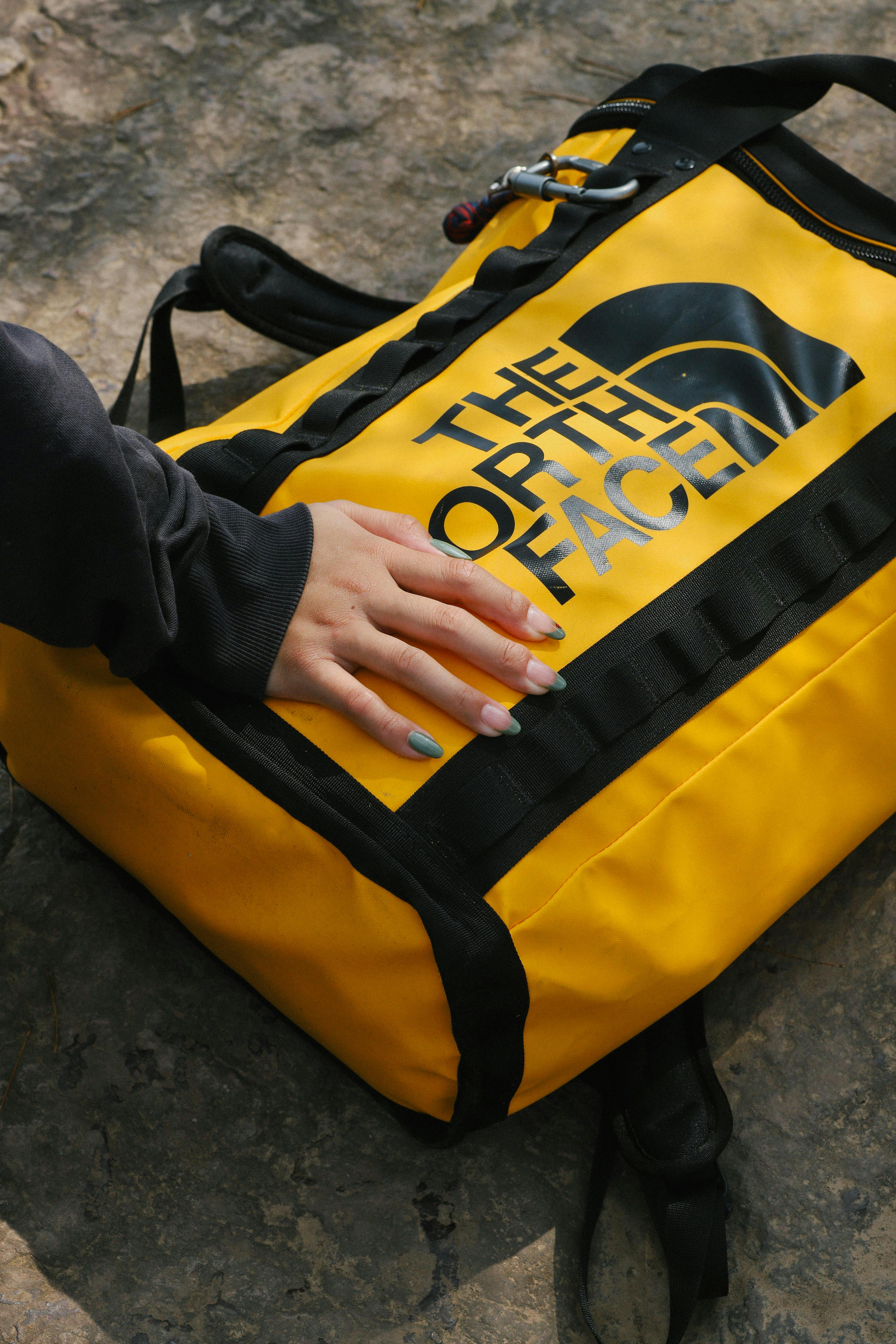 Yellow North Face Backpack with Hand on Stone Surface · Free Stock Photo